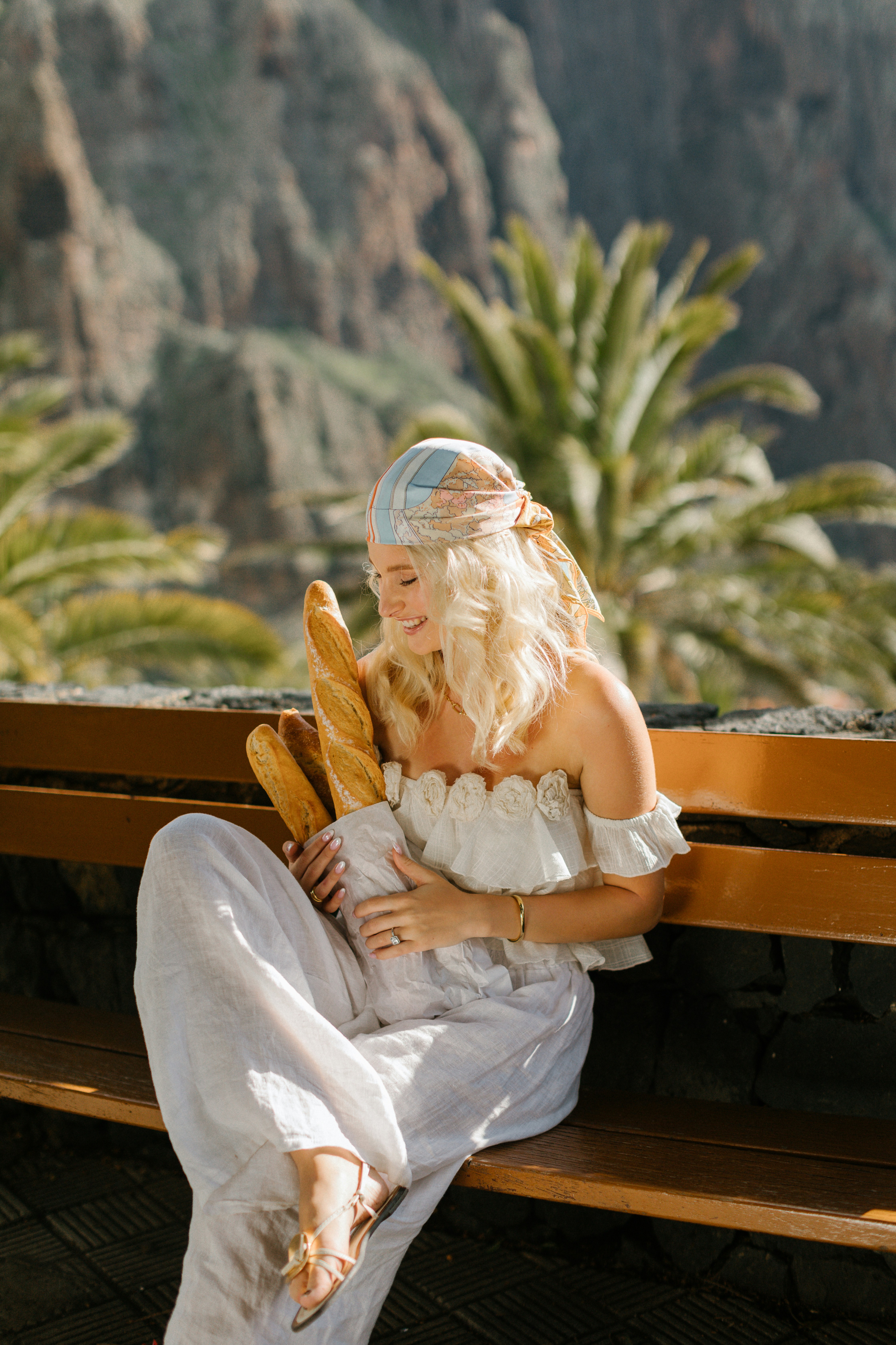 Sunlit Bakery Moment: A Woman in White with Baguettes on a Park Bench