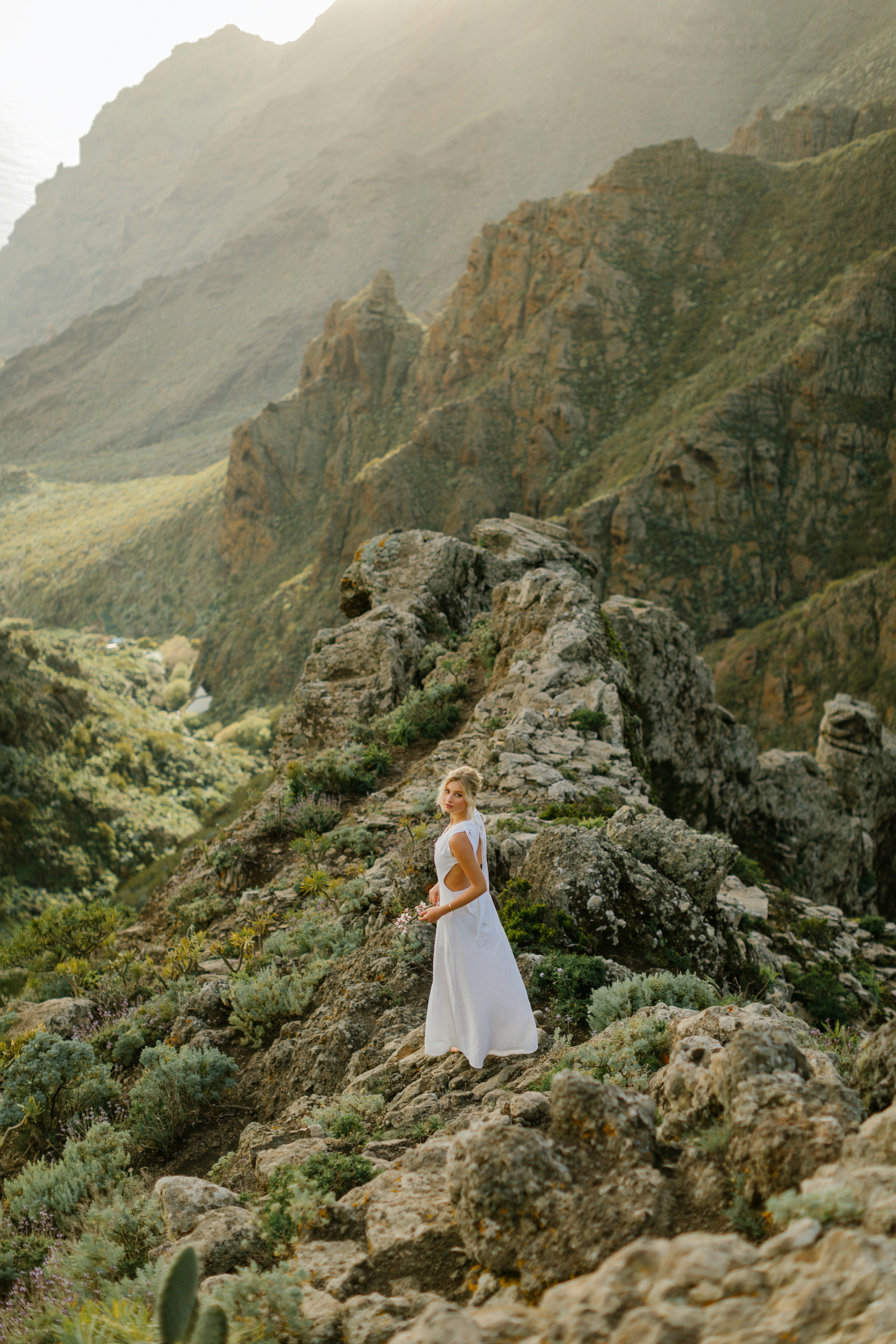 White-dressed wanderer on rugged cliff edge beneath sunlit canyon
