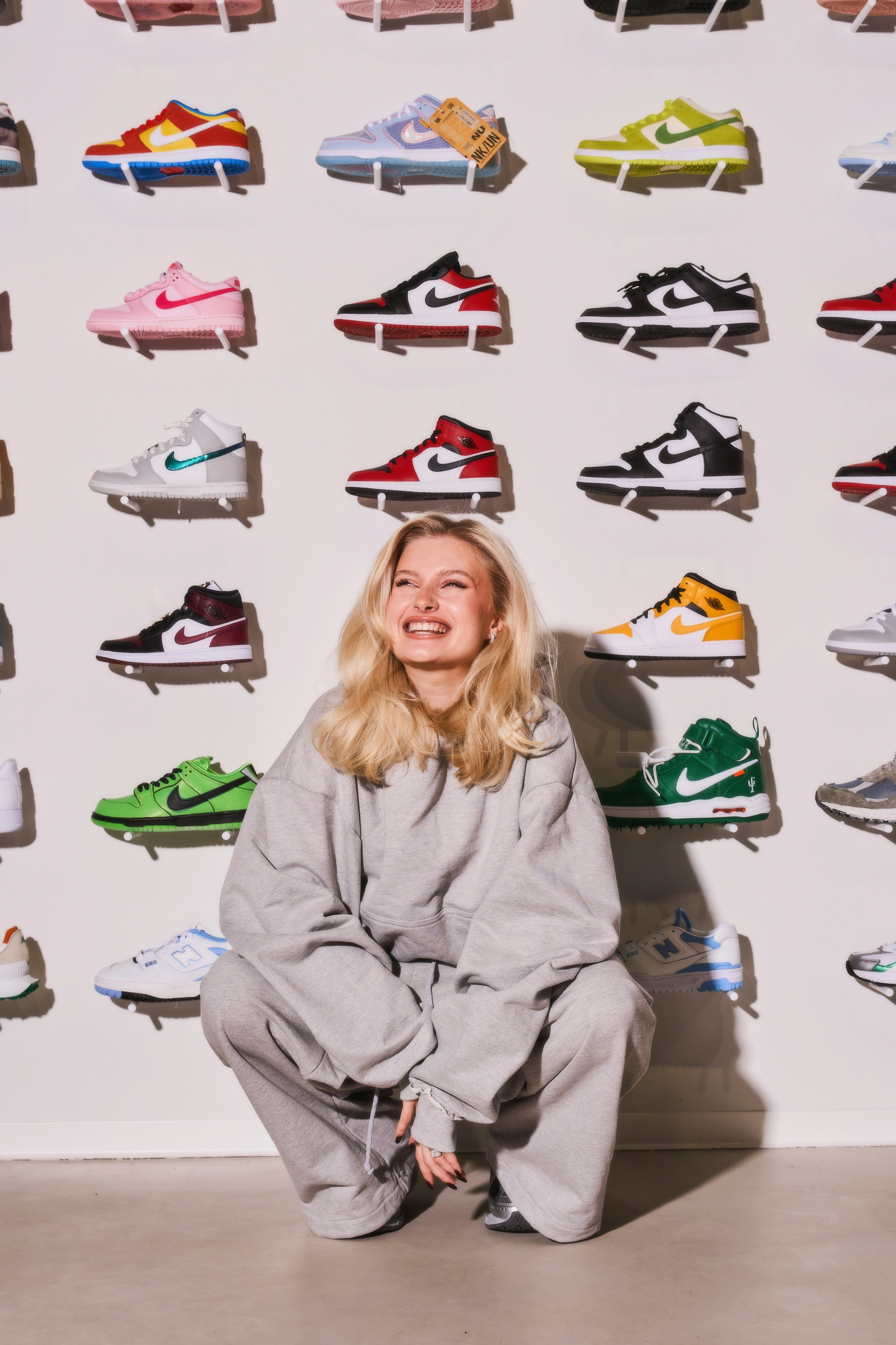 Blonde in a Cozy Squat Amid a Wall of Colorful Sneakers