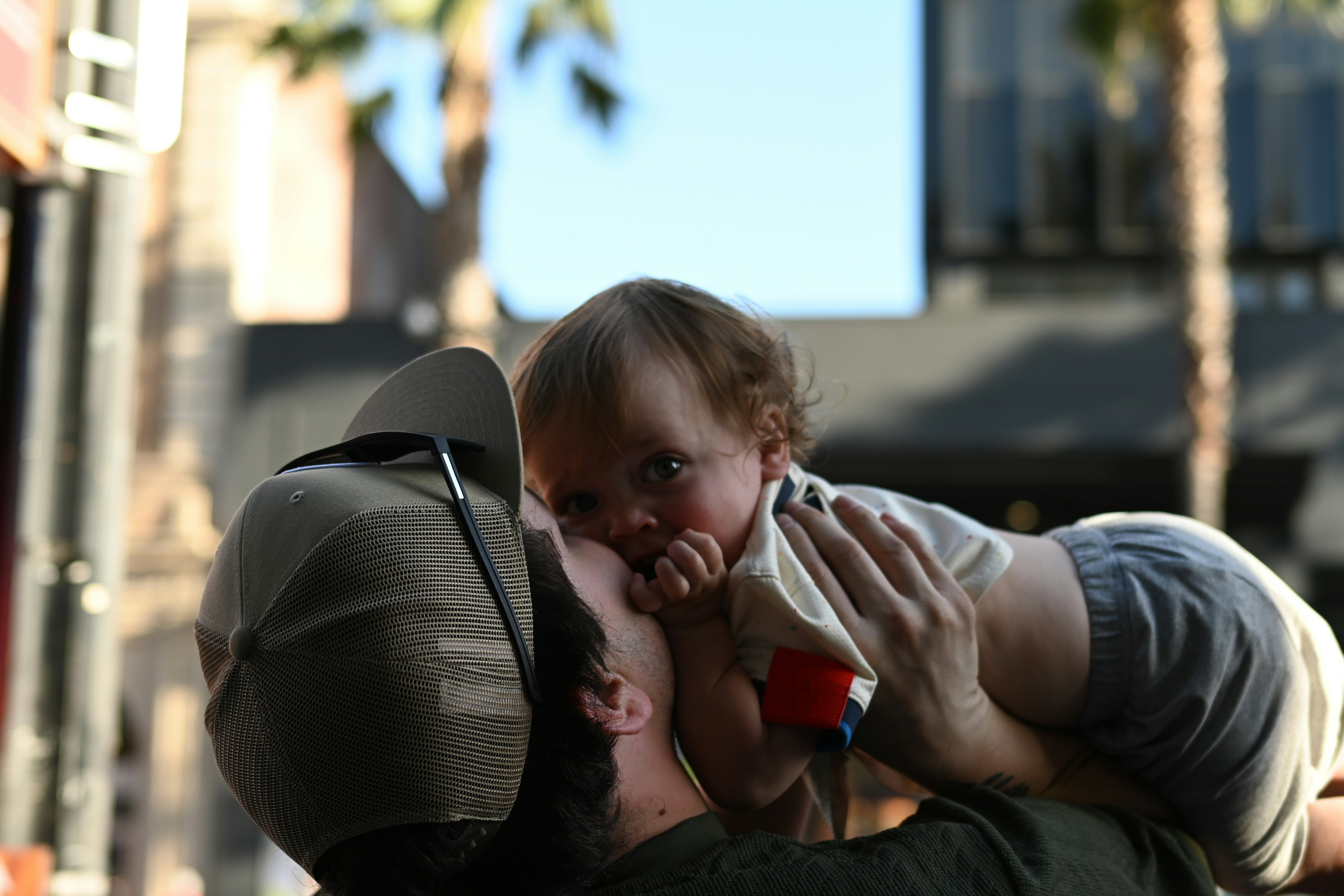 Tender Lift: A Father’s Embrace and Baby’s Curious Gaze