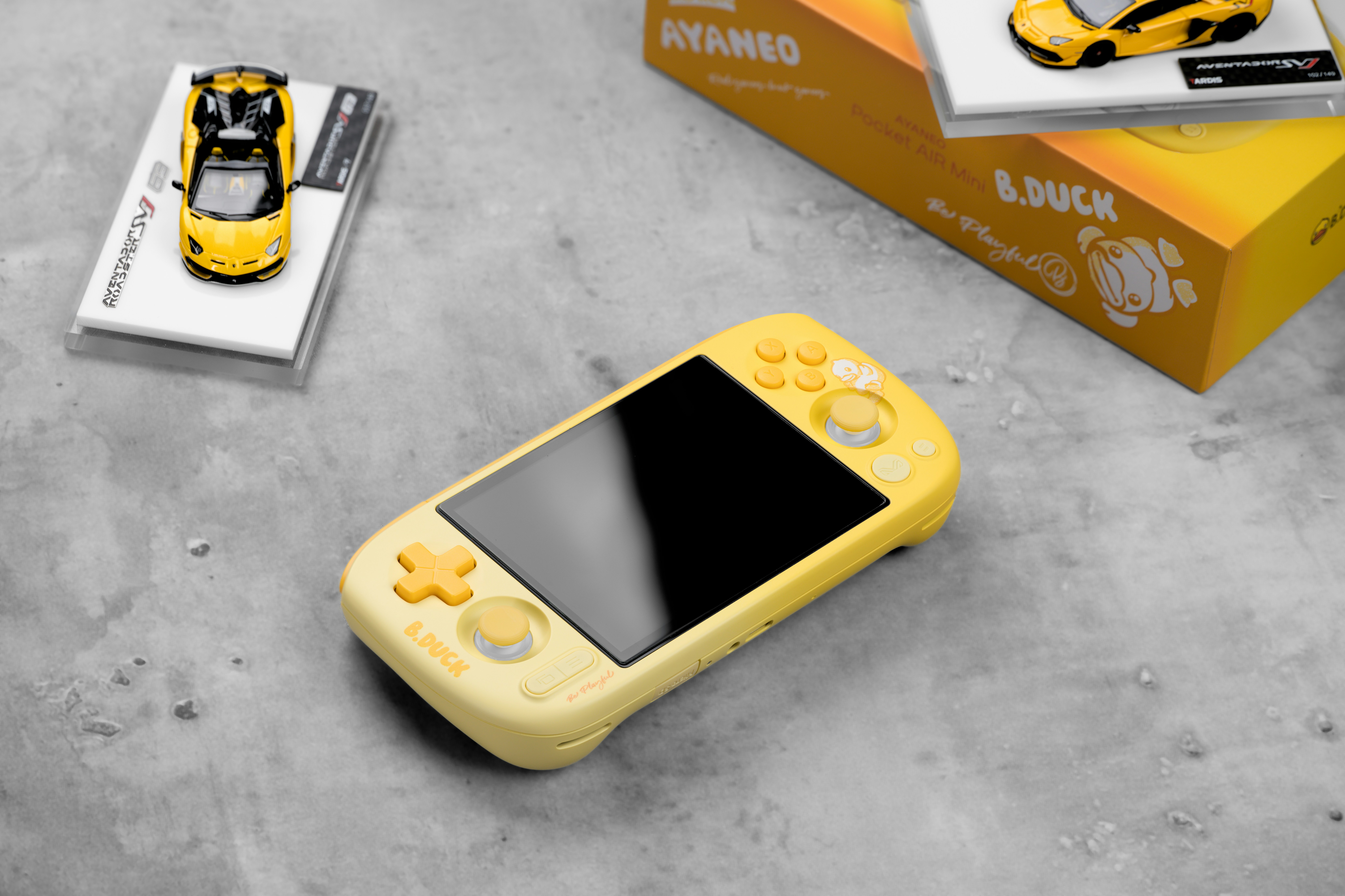 Sunny handheld nostalgia: a yellow gaming console amid boxed car models