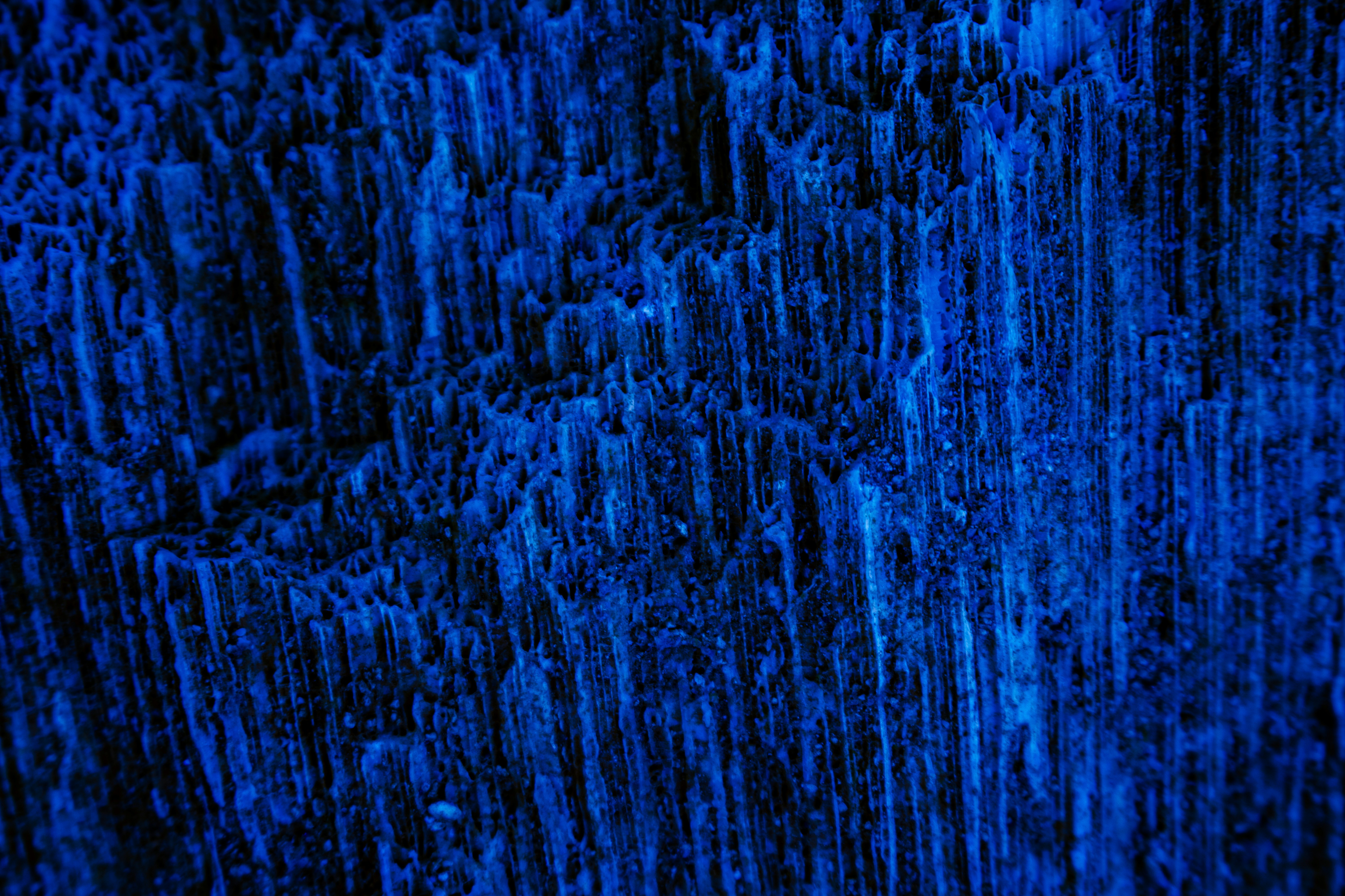 Ultramarine ice-like ridges forming vertical textures across a blue-toned surface. Abstract macro landscape with pronounced vertical grooves and cool color palette.