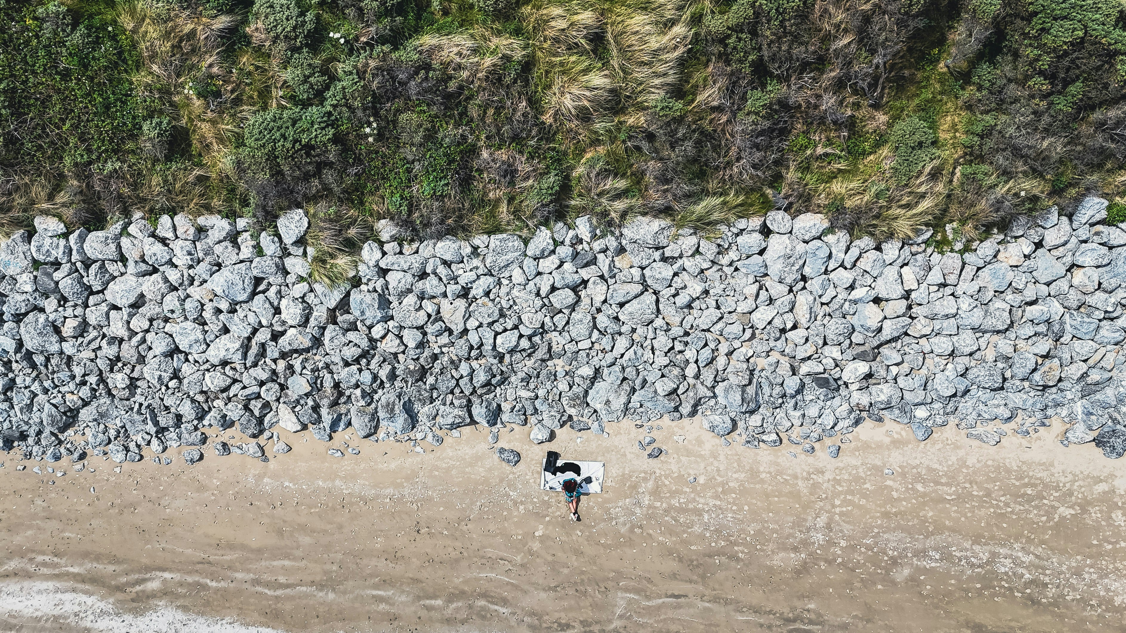Beachside Drone Portrait: A Lone Figure Anchored by Pebbles and Rocks