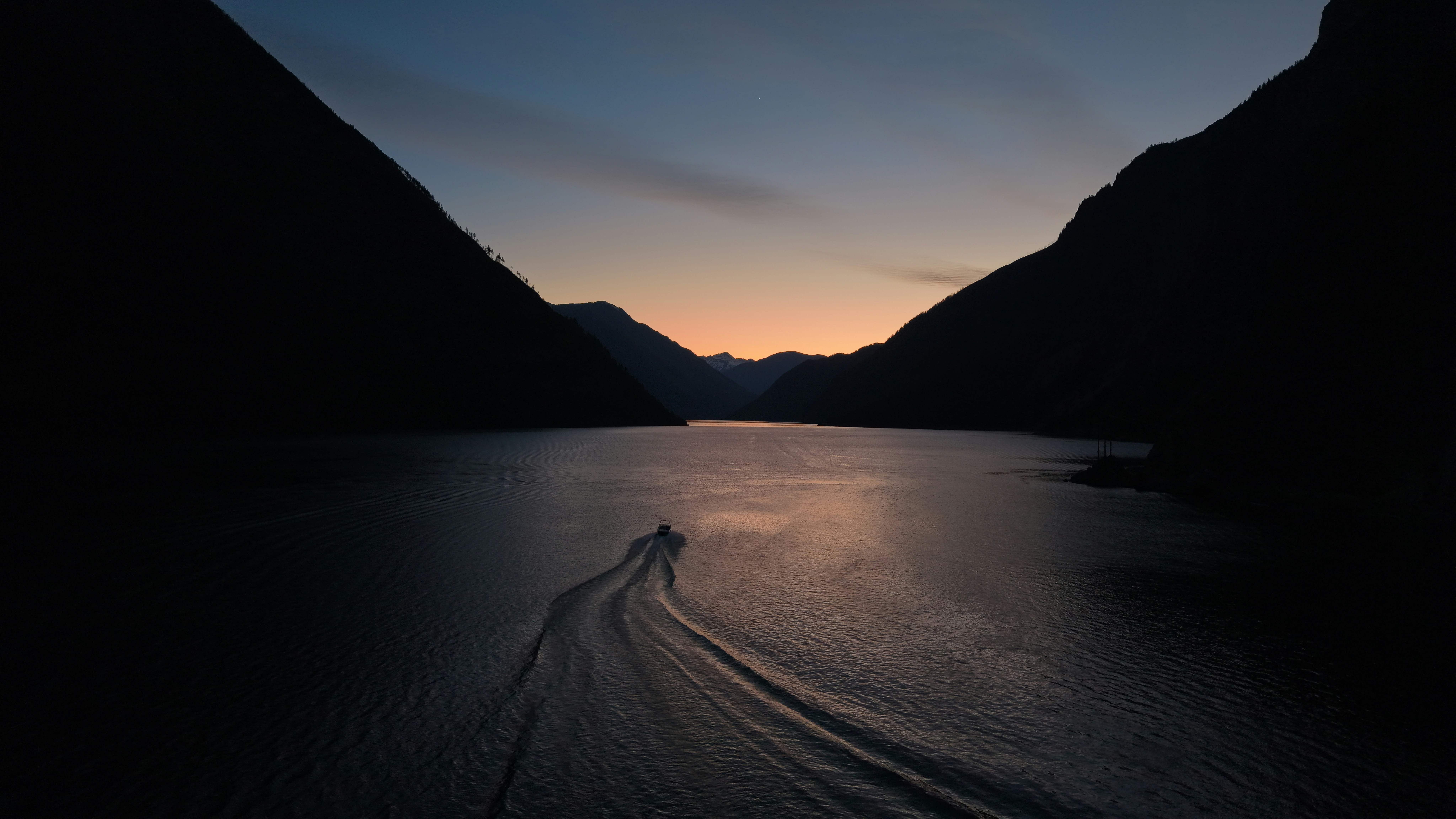 Silhouette Passage: A Boat Traces Quiet Wake Through Mountain Fjord at Dusk