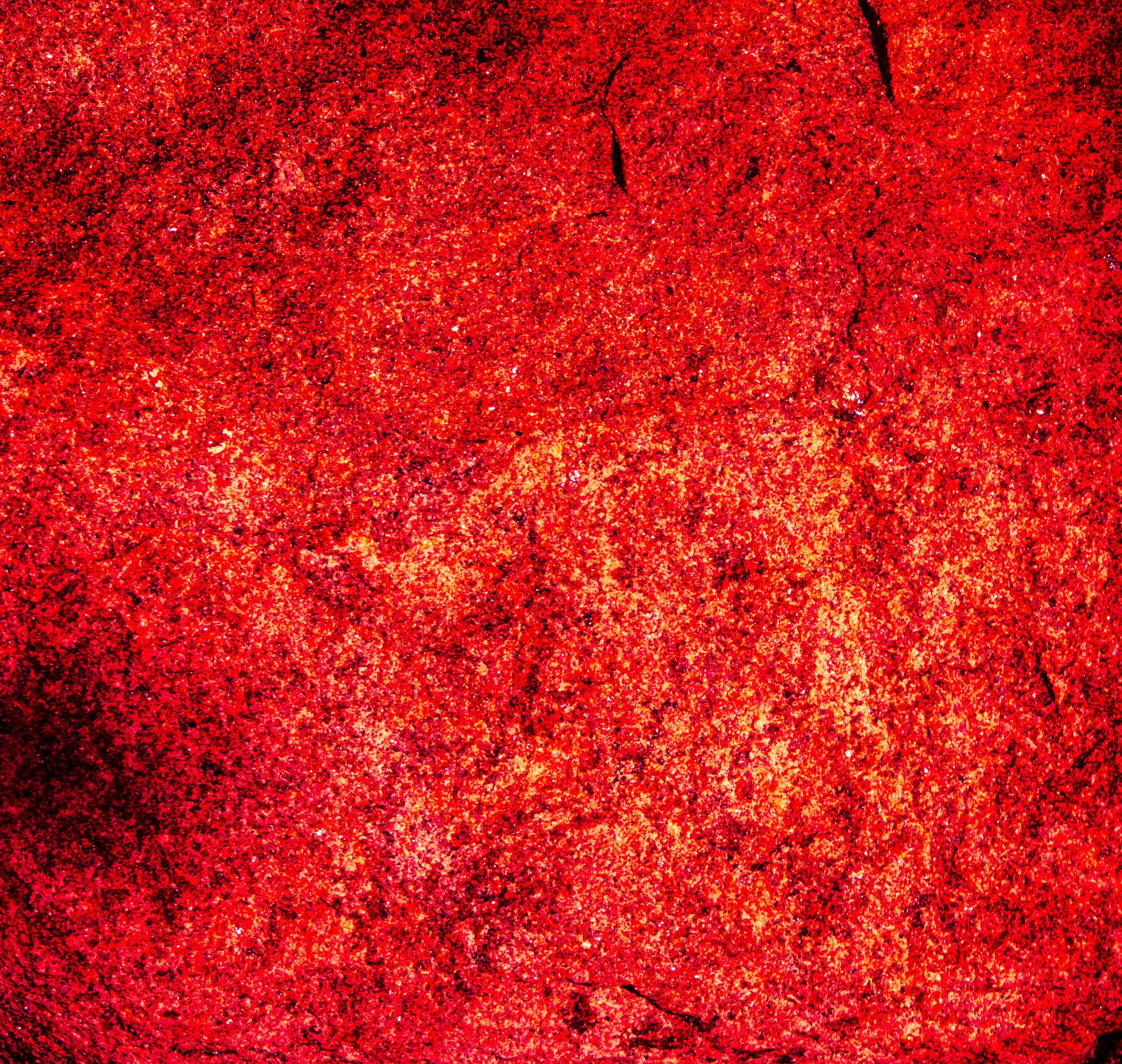 A close-up of a fiery red textured surface with mottled orange highlights and dark shadows, presenting a rich, tactile pattern. (This is a photographic texture, not a natural scene.)