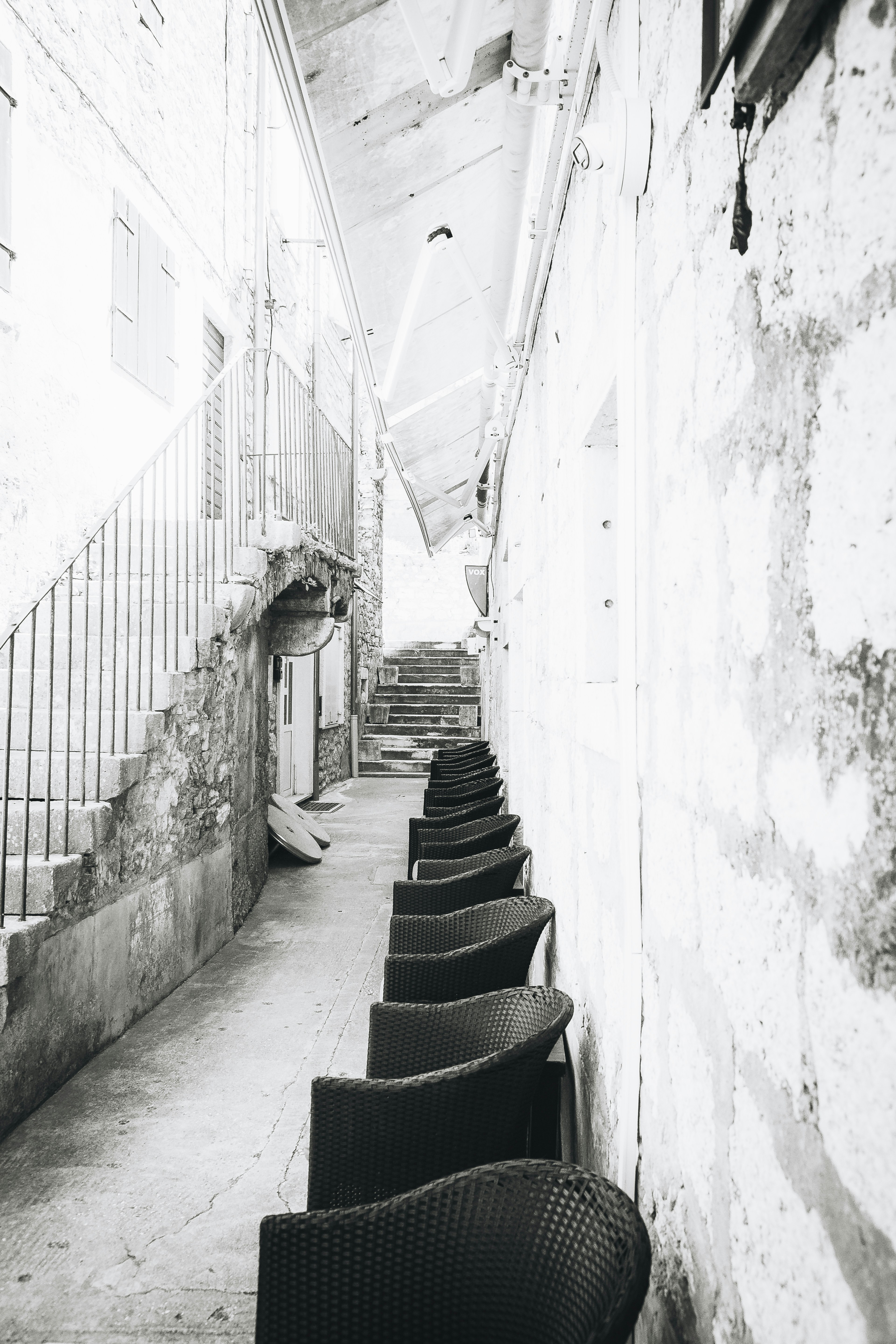 Narrow alleyway lined with stacked chairs receding toward a bright apex