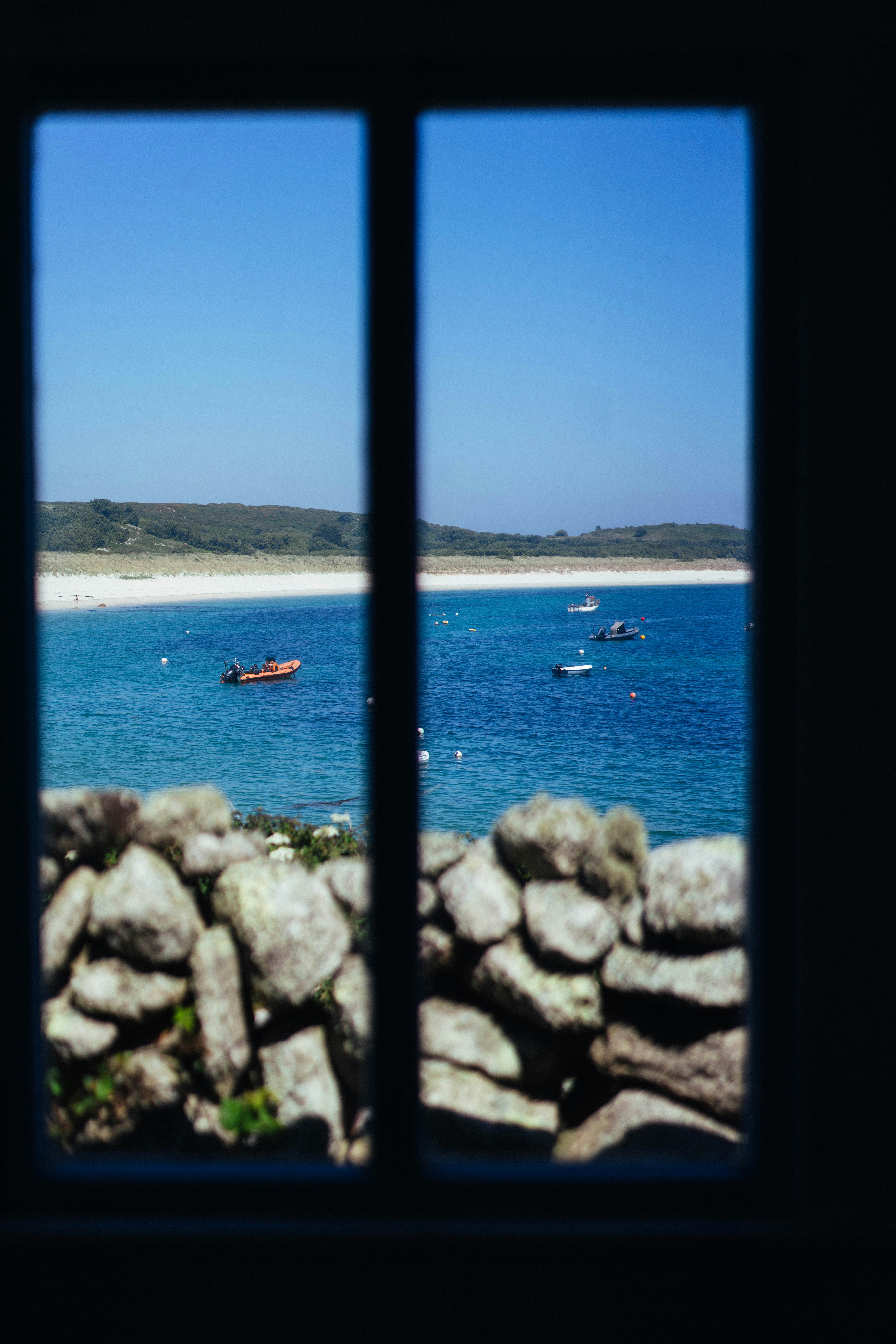 Sea View Through a Narrow Window: Boats, Blue Water, and a Stone Wall
