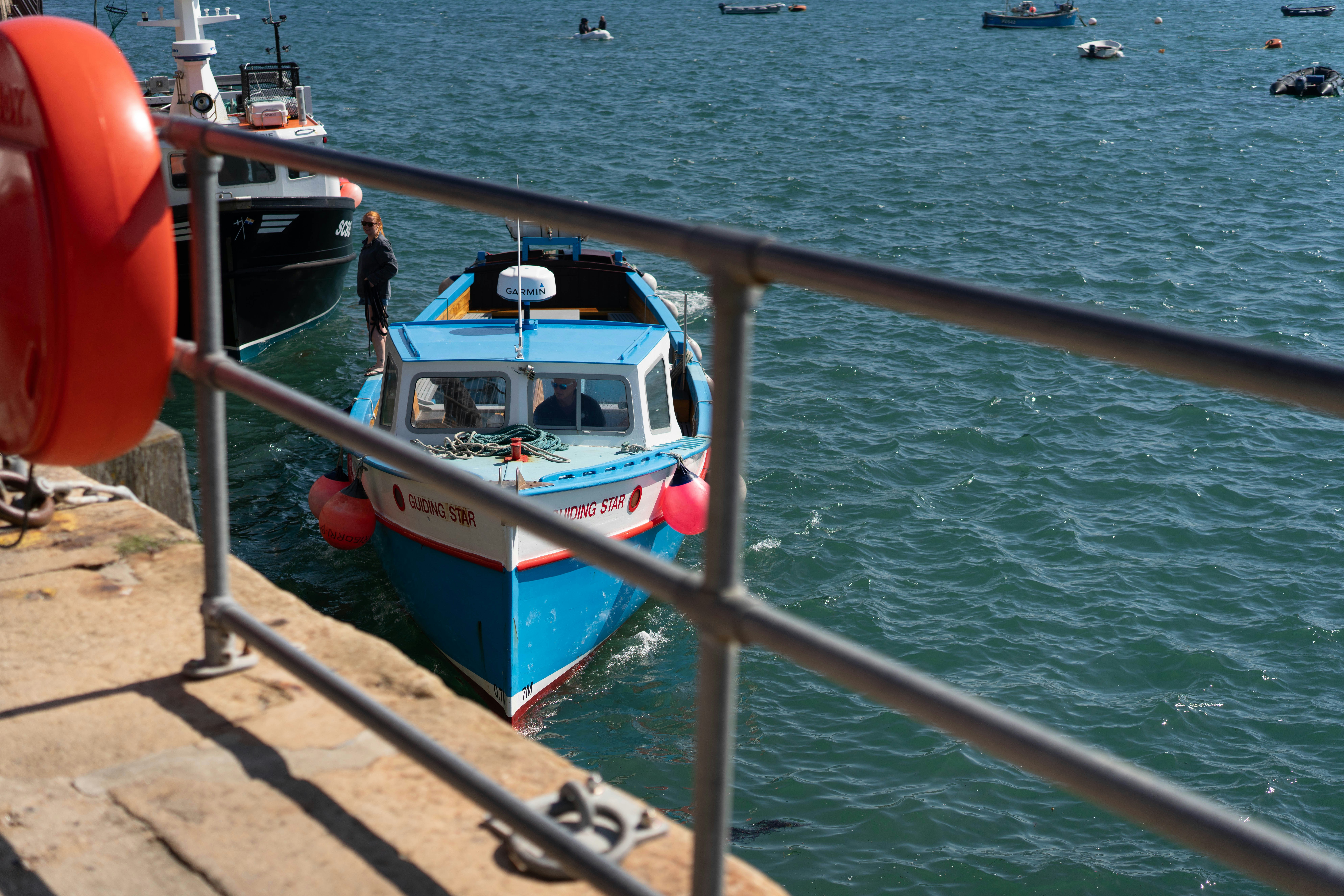 Blue boat at the quay framed by railings on a sunlit harbor
