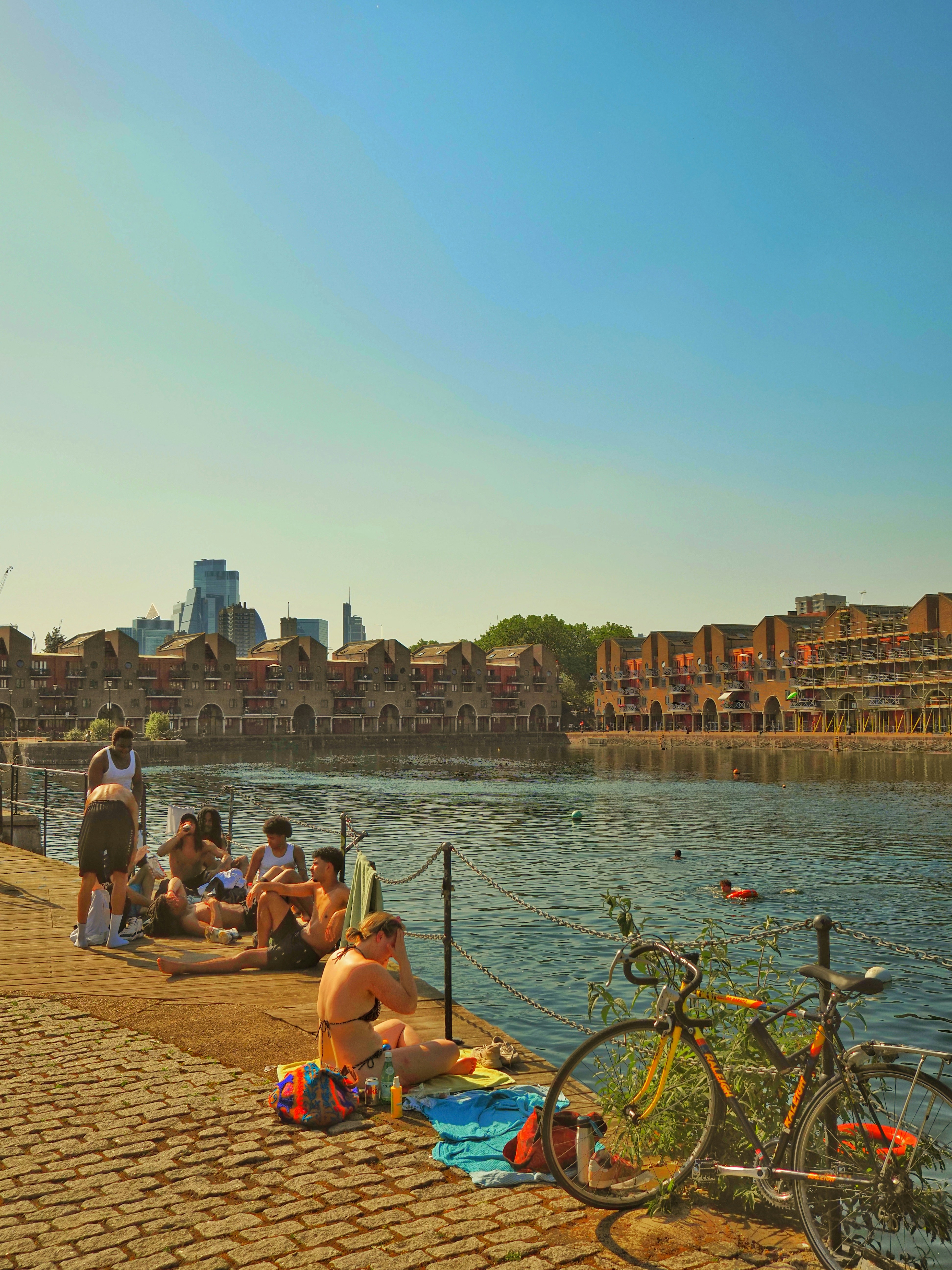 Sunlit Riverside Social: Beachgoers and bicycles by the quay