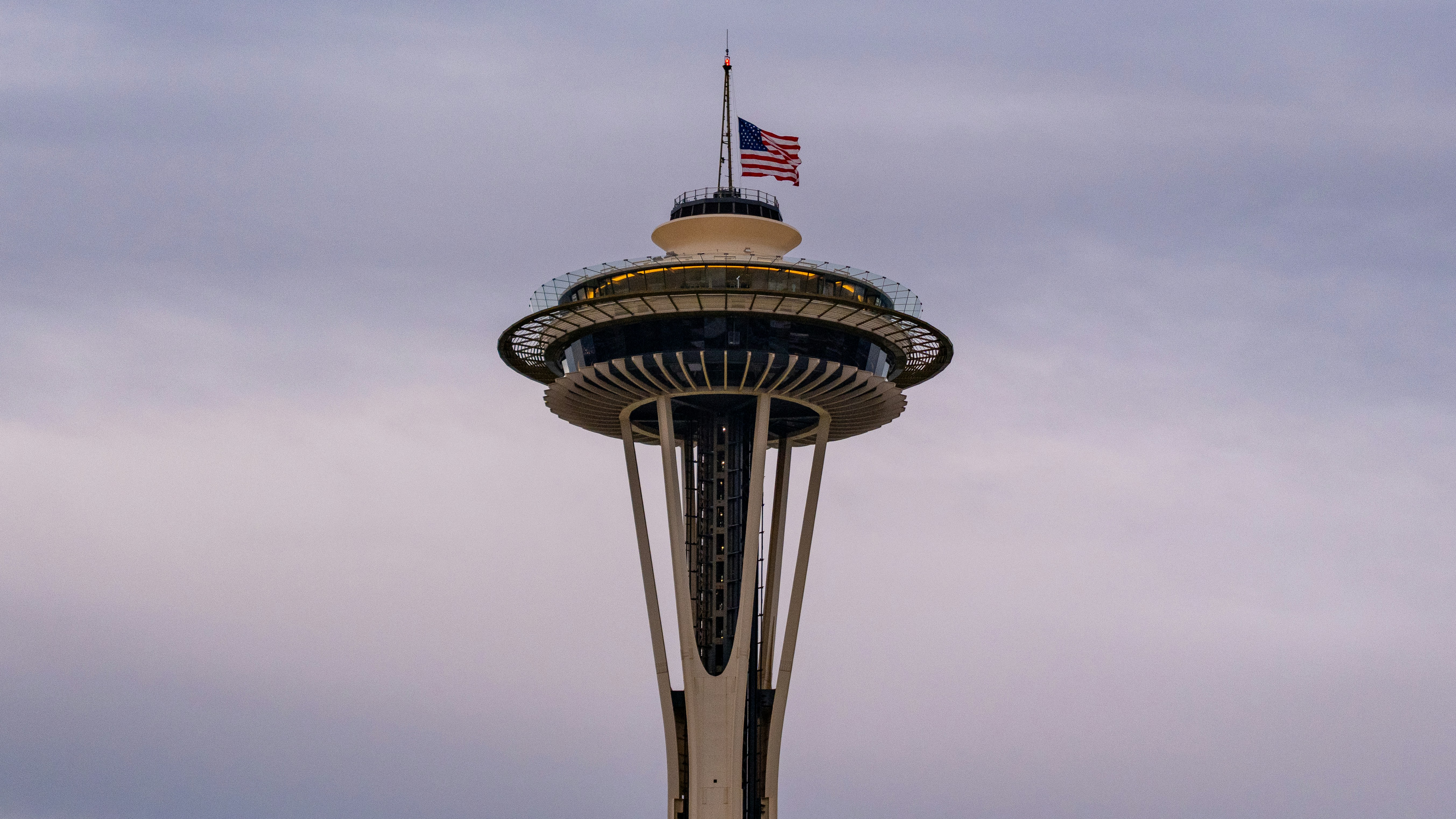 Flag atop a midcentury observation tower piercing a pale sky