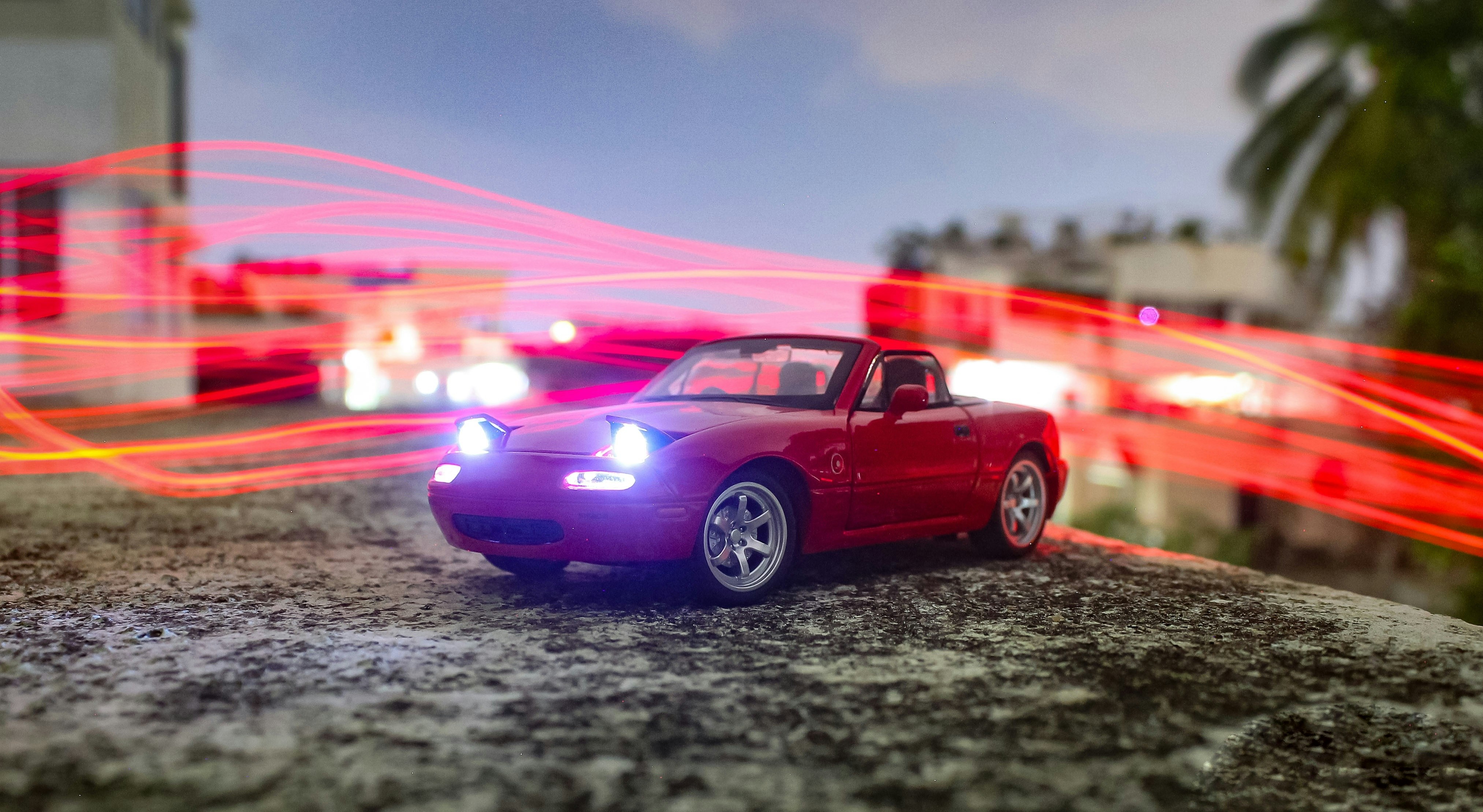 Red toy car streaked with light trails under a night sky