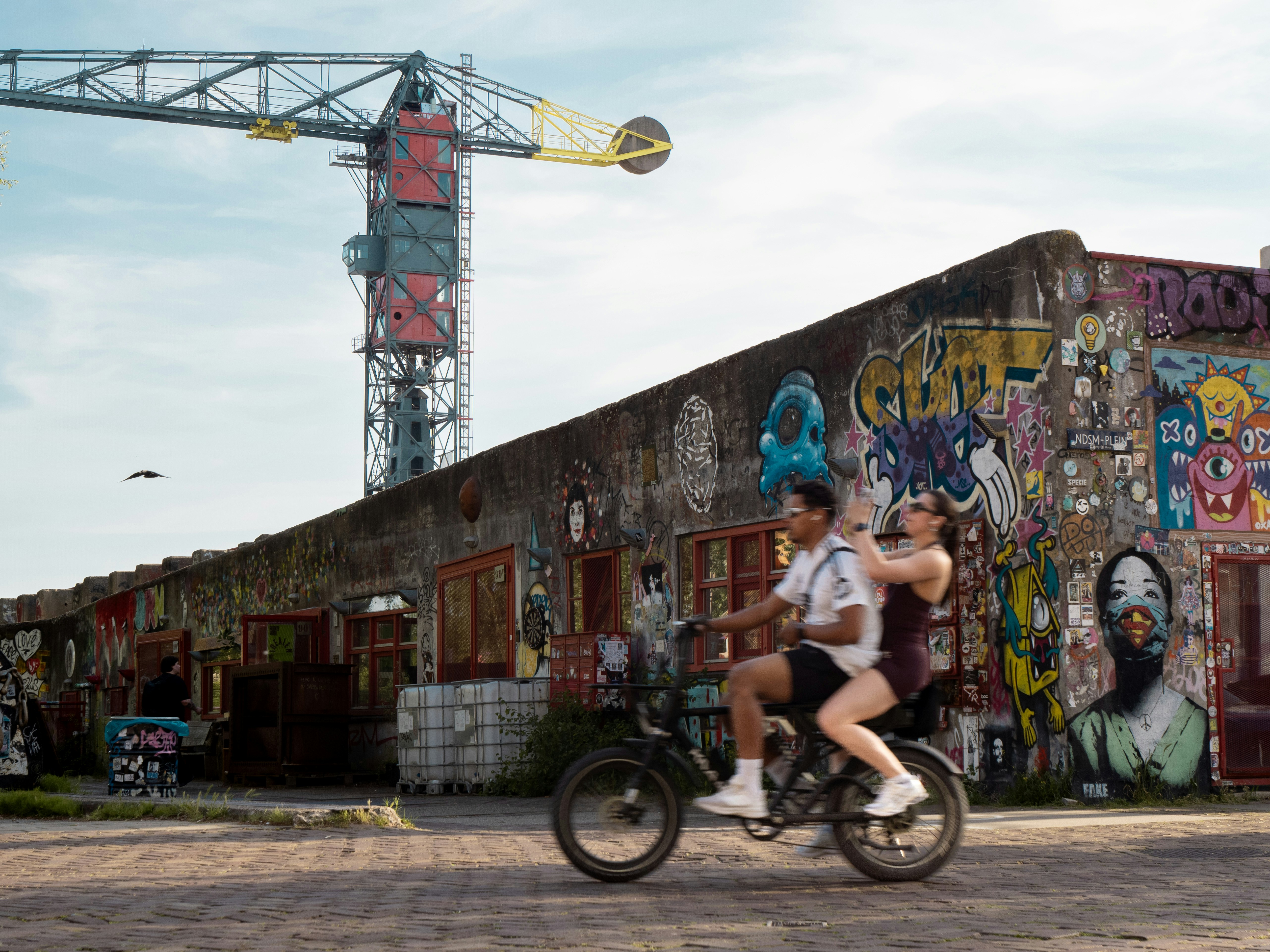 Rider duo in motion before a graffiti-clad wall under a construction crane