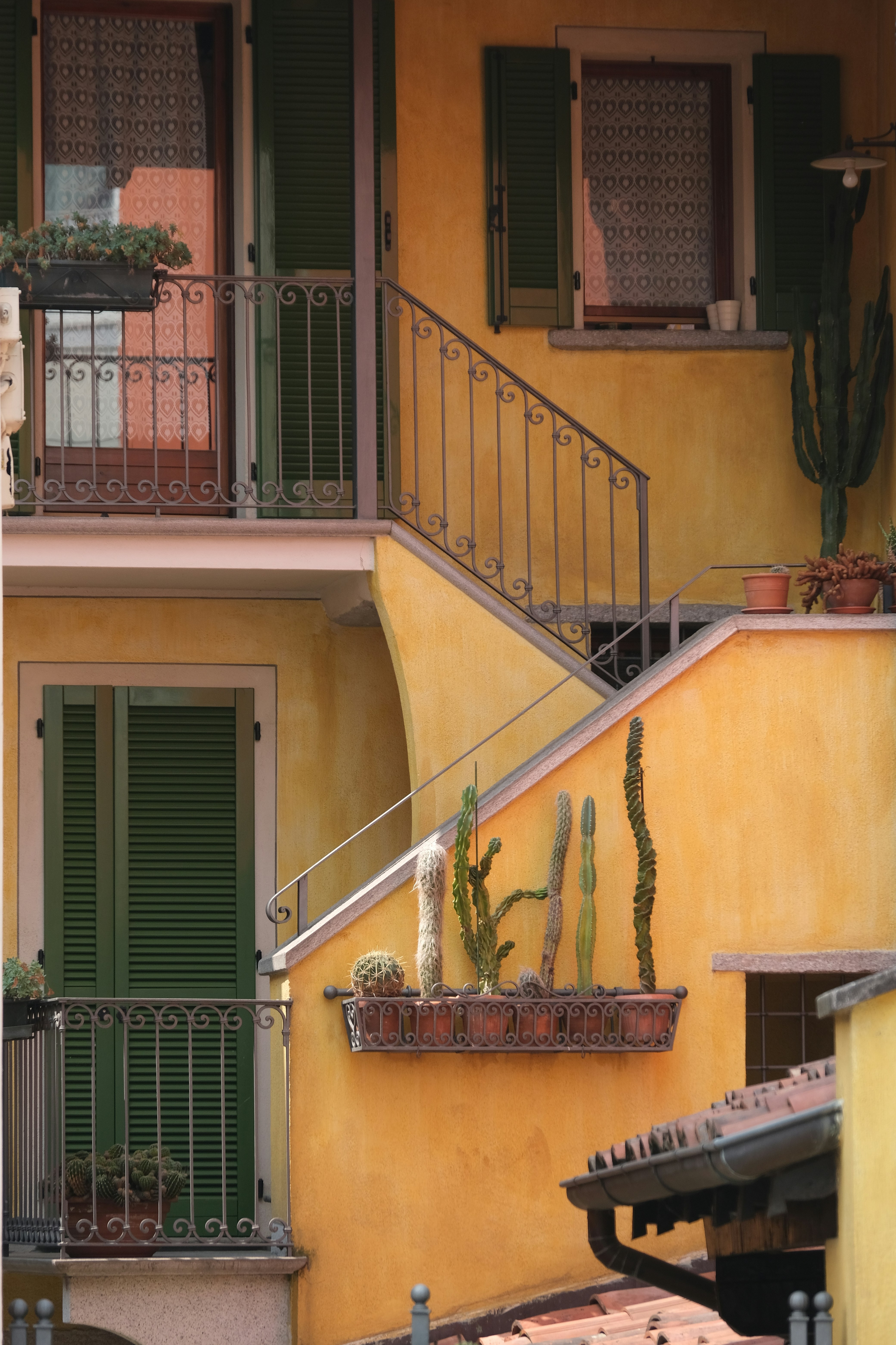 Sunlit Yellow Courtyard Stairway Weaving Through Green Shutters