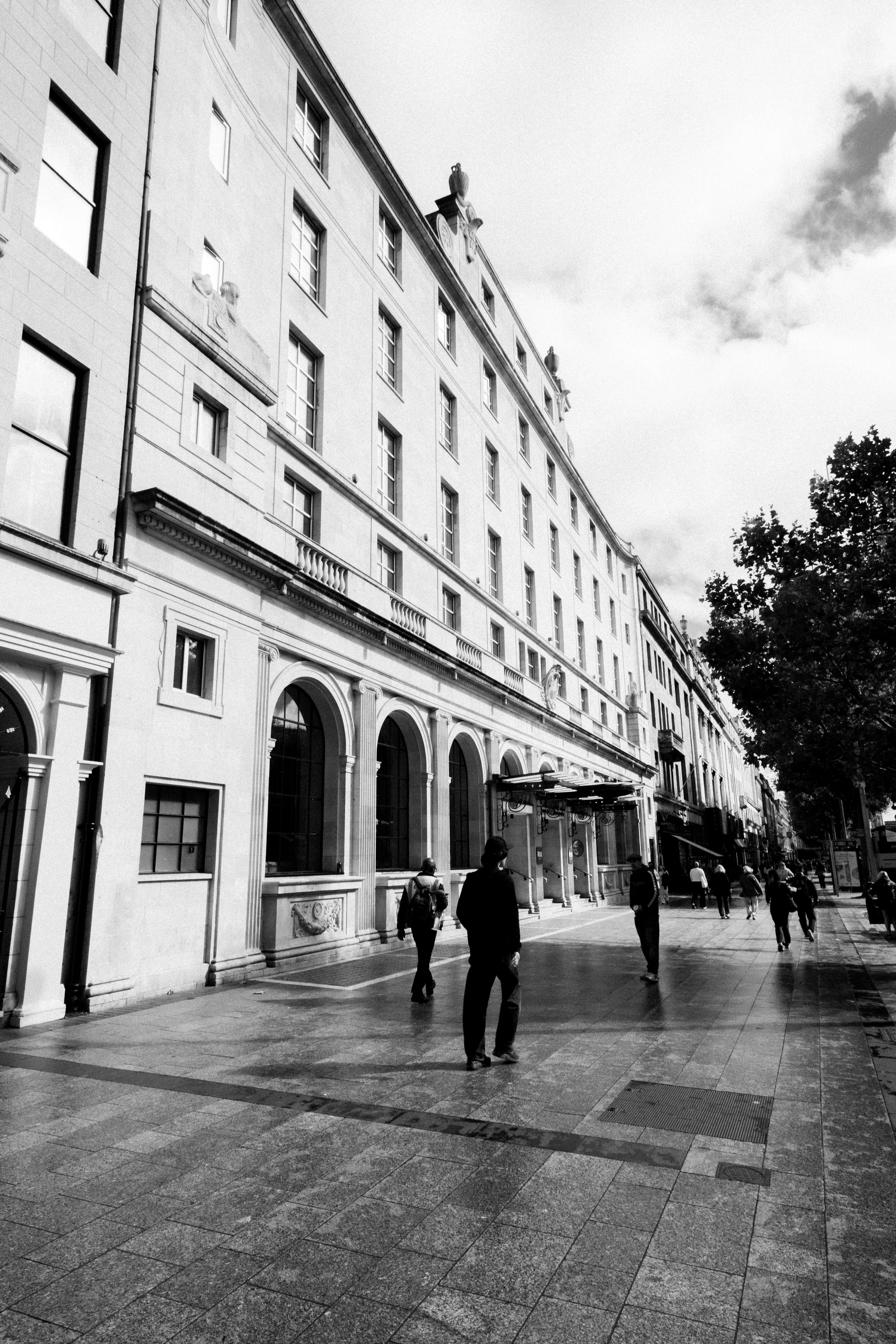 A Soho Street Quietly Rushes by: People and Arches in Evening Light