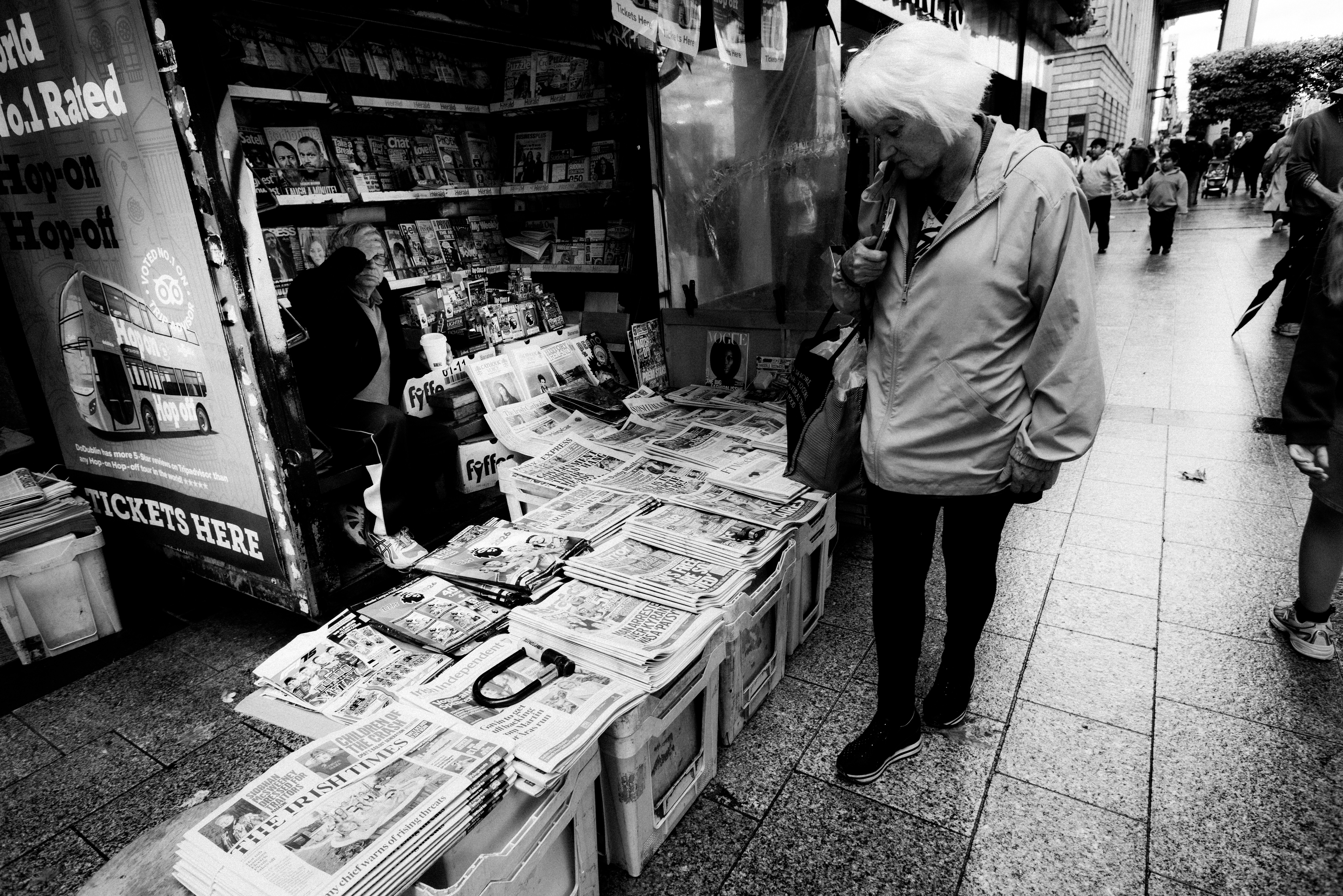 Elderly woman browsing newspapers at a street newsstand.