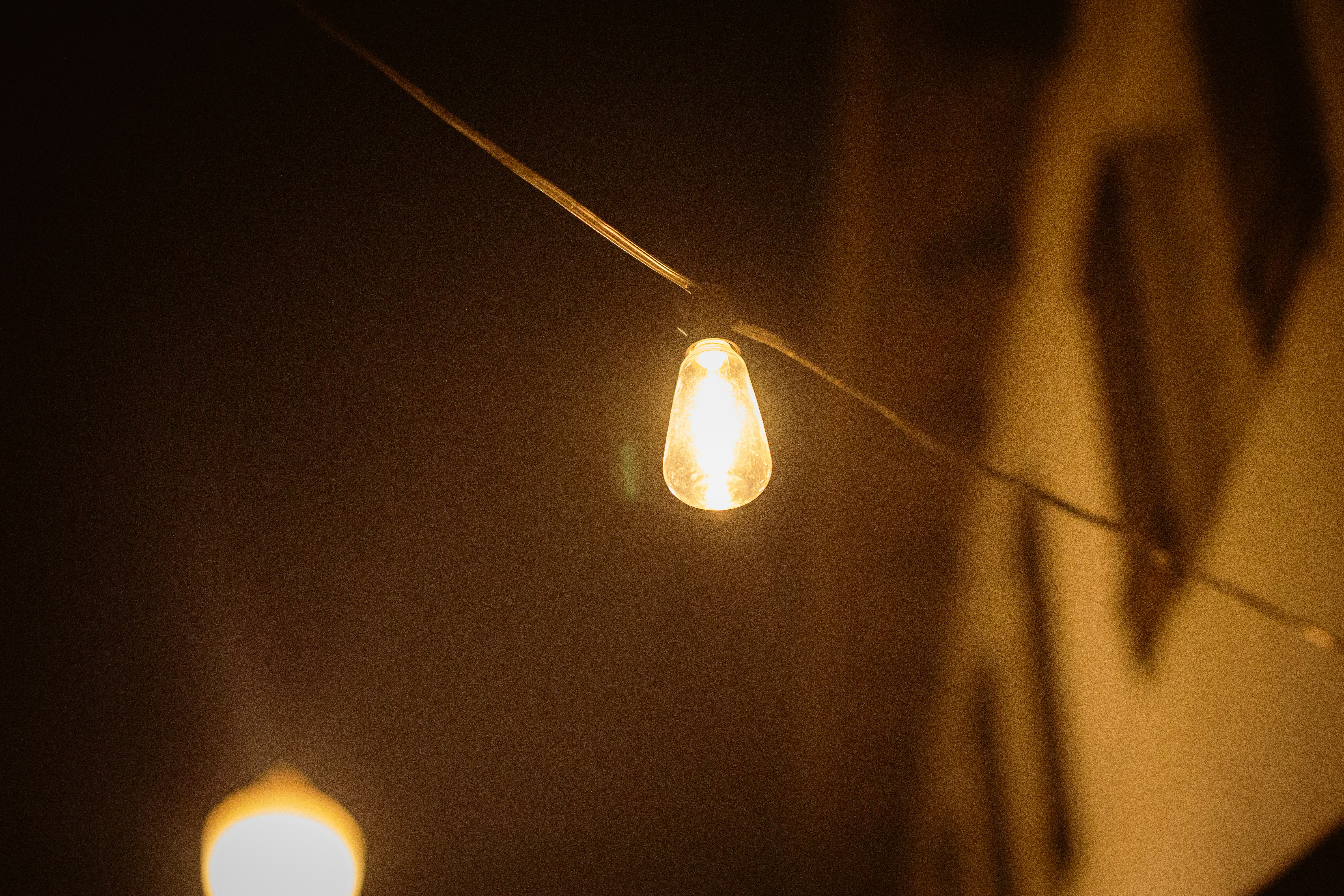 A solitary bulb glows in the evening haze, tethered by a thin wire