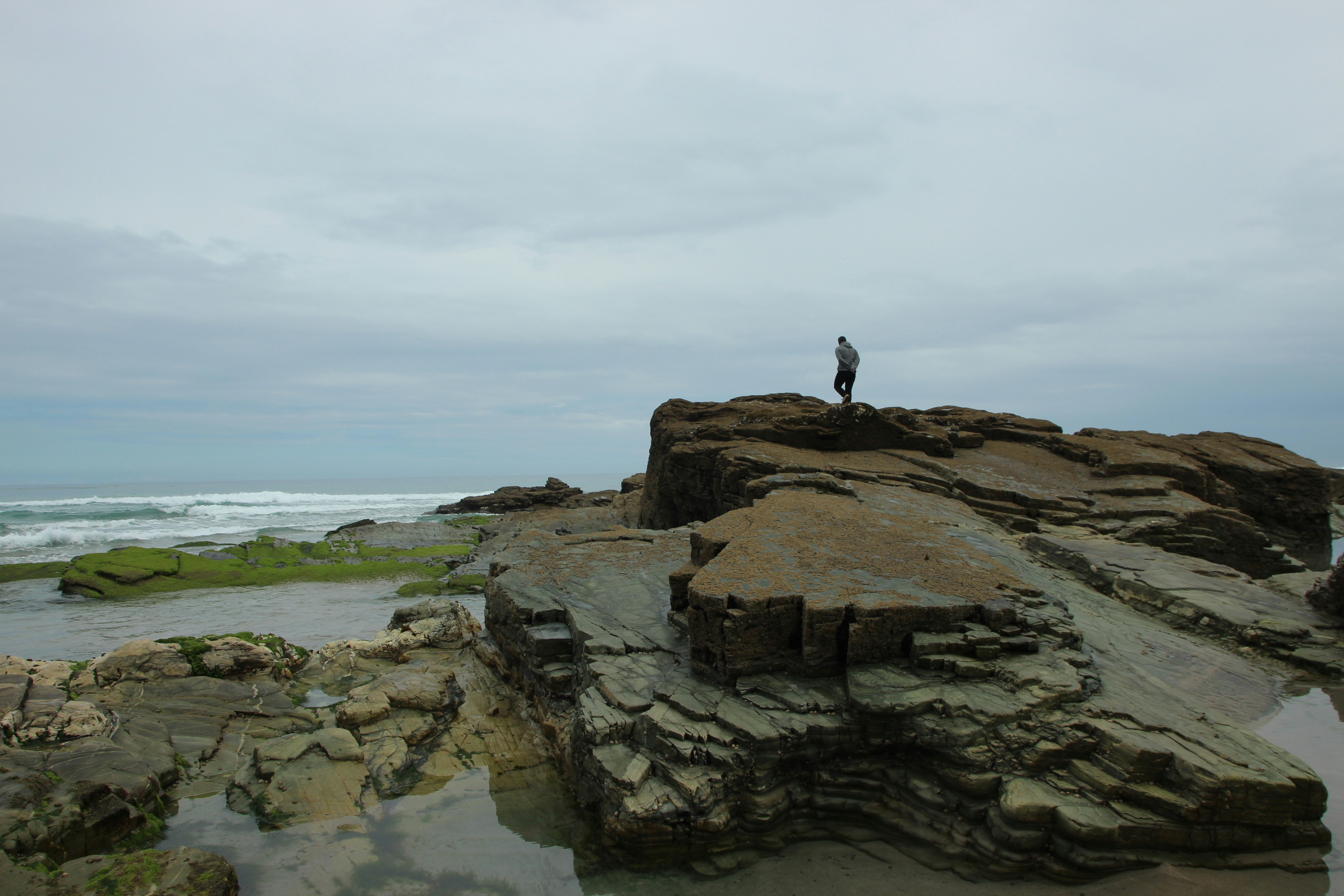 Figure on jagged coastline rock under a broad sea-sky expanse