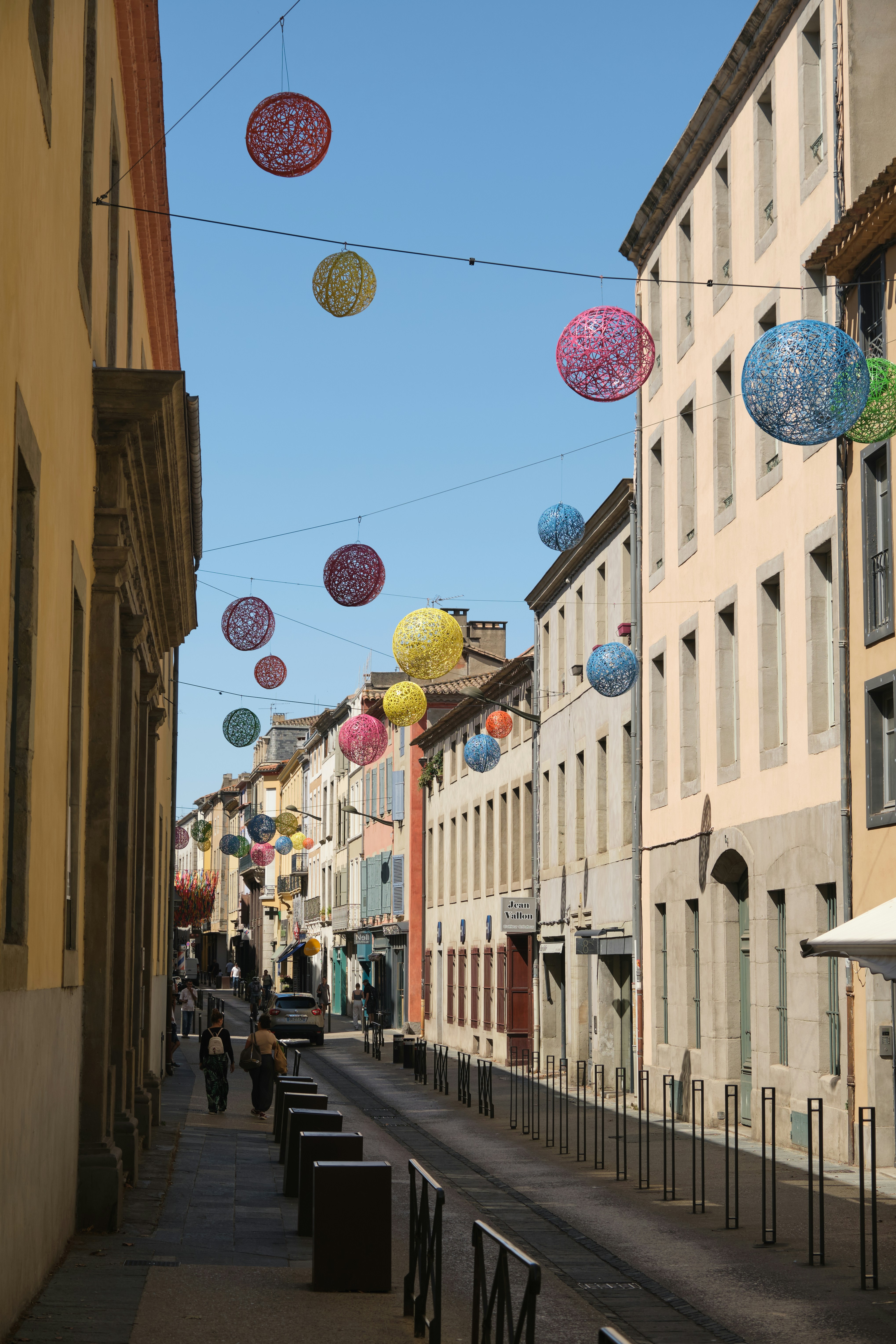 Streetscape of Floating Orbs: A Sunlit Corridor of Colorful Ornaments
