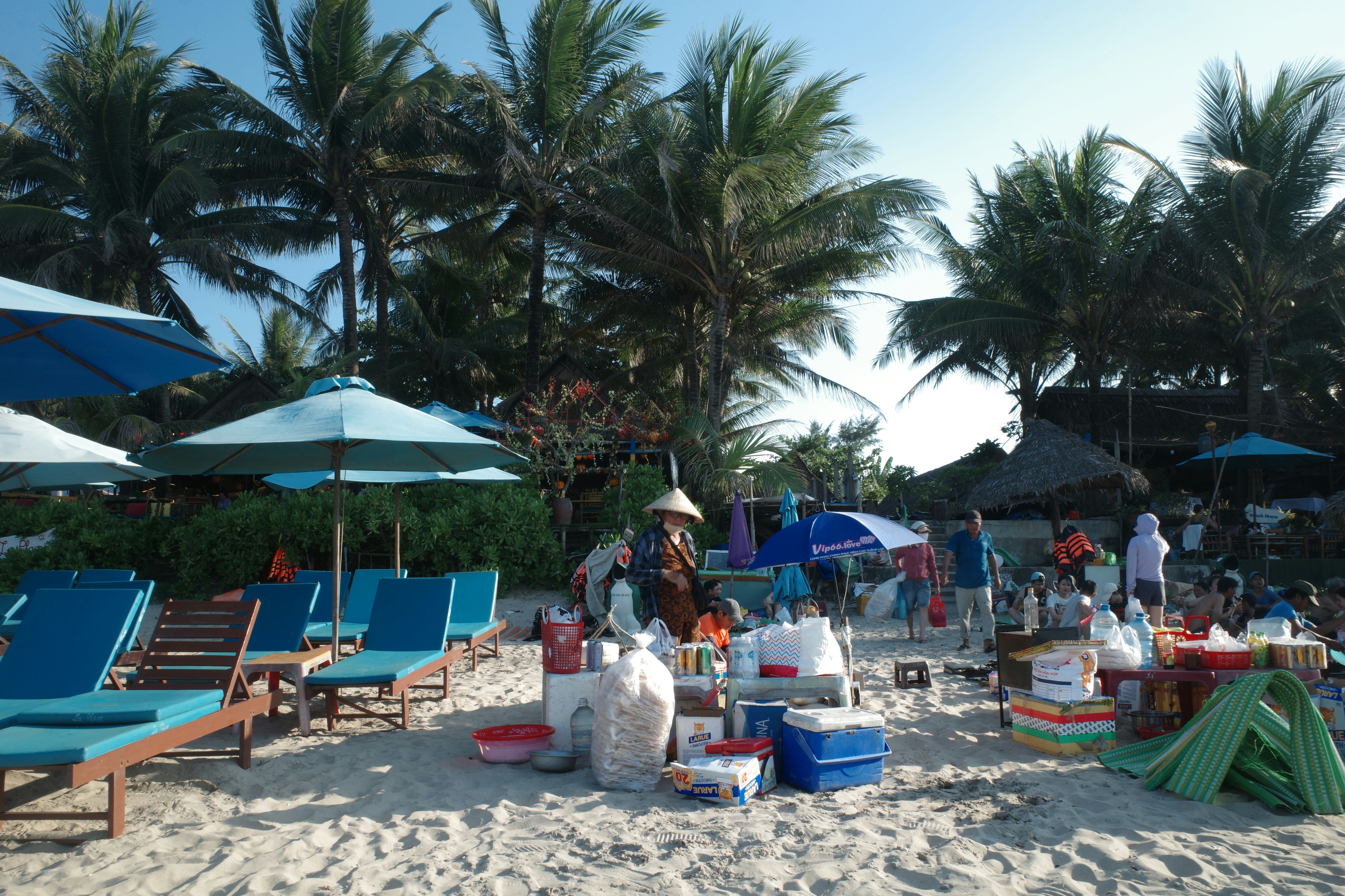 Beach Market at Dusk: Traders and Turquoise Umbrellas Under Palm Skies