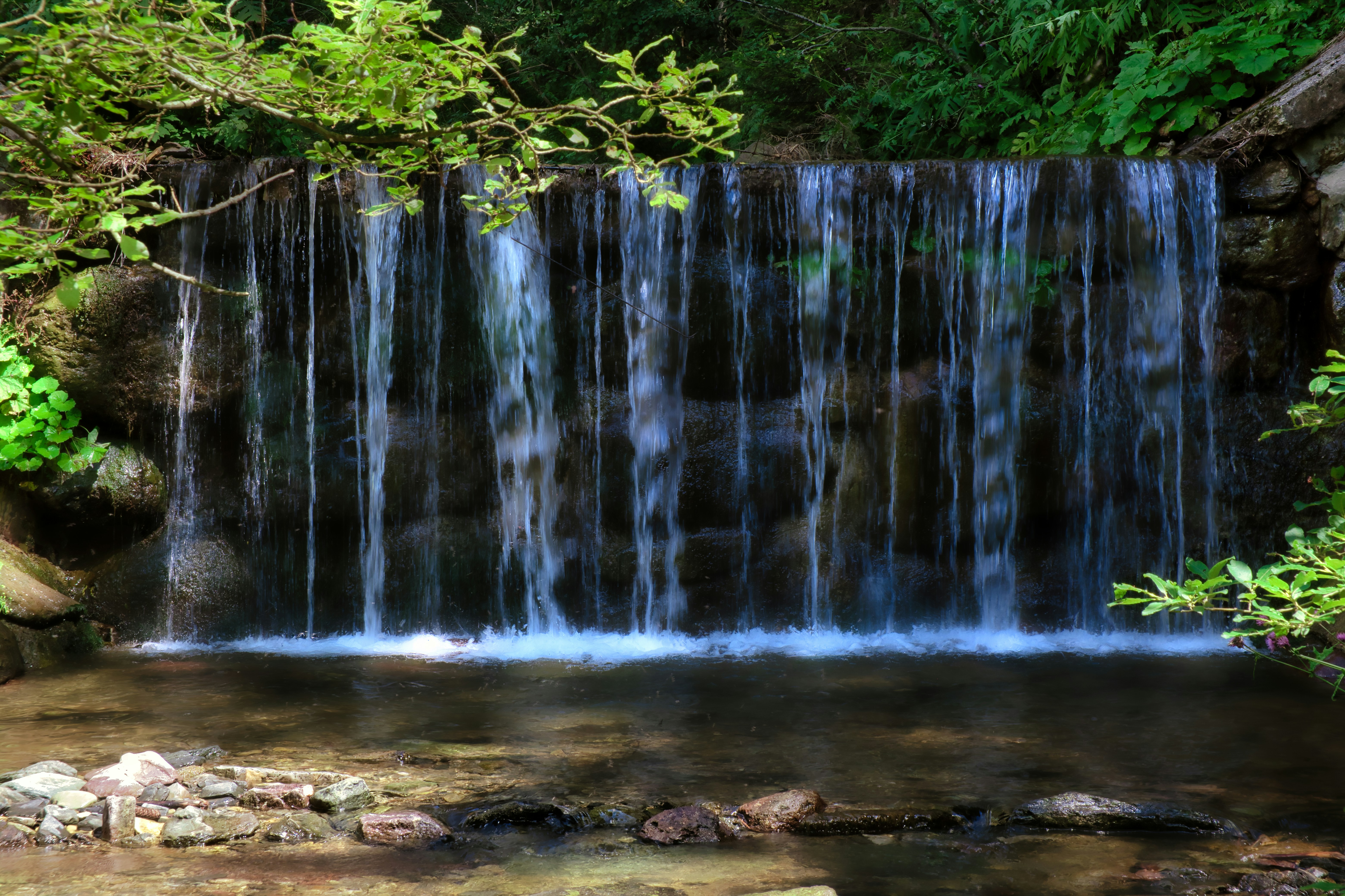 Quiet Cascade: A Riverside Curtain Over Pebbled Banks