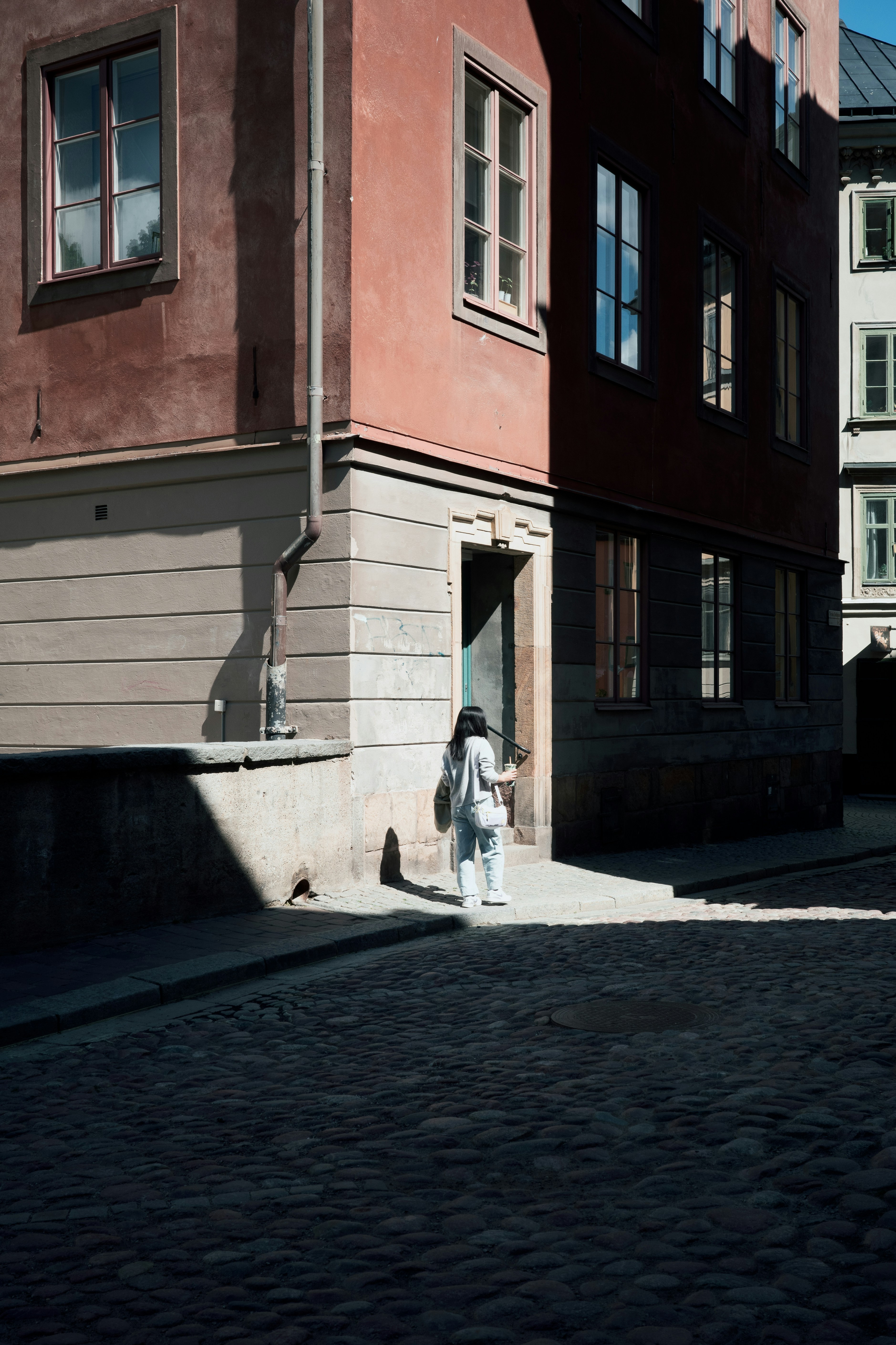 Woman in Light Coat at a Sunlit Townhouse Door