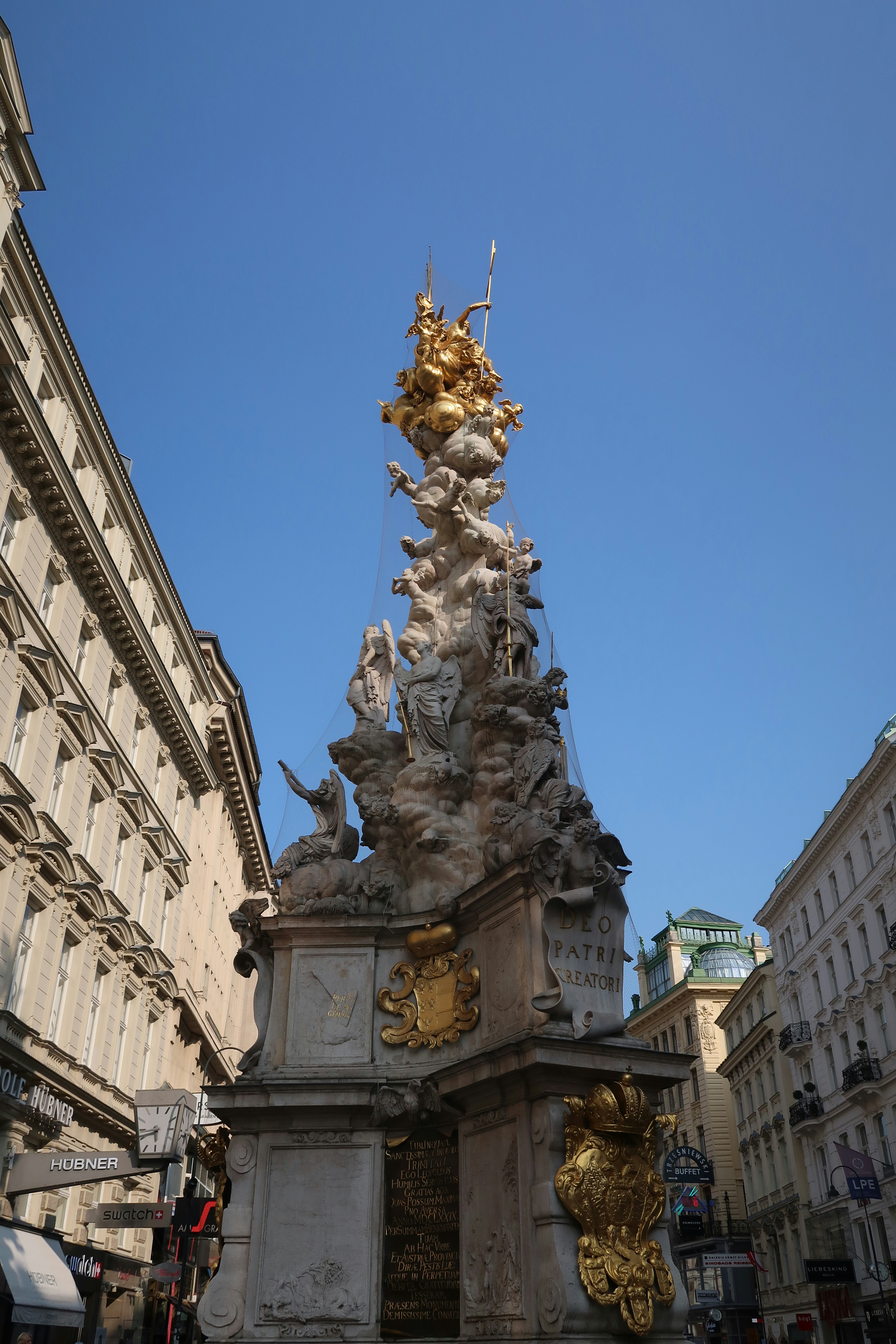 Golden apex: the statue blaze atop a Baroque monument against a clear city sky