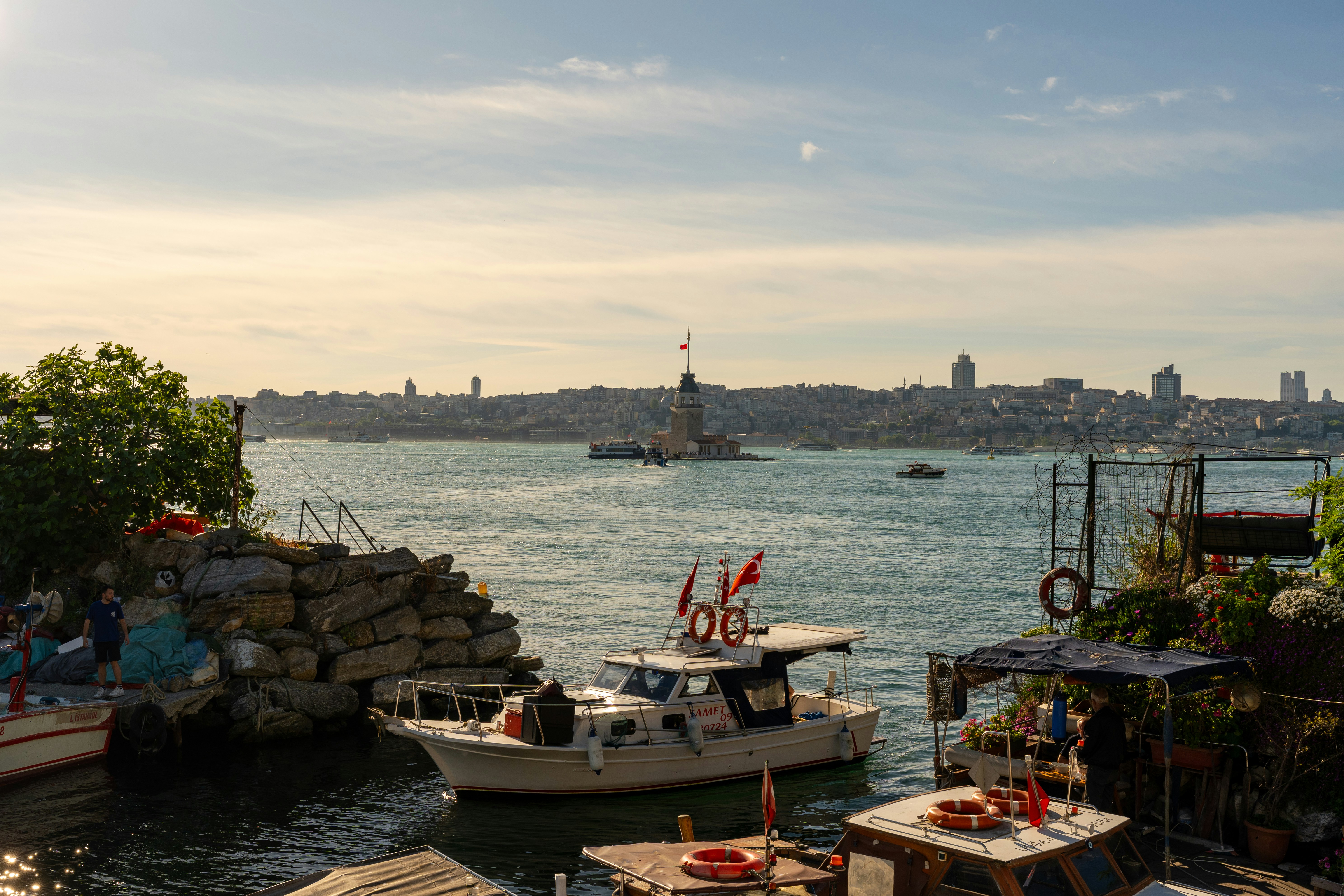 Harbor Scene at Dusk: Boats, Rocks, and a Distant Waterfront