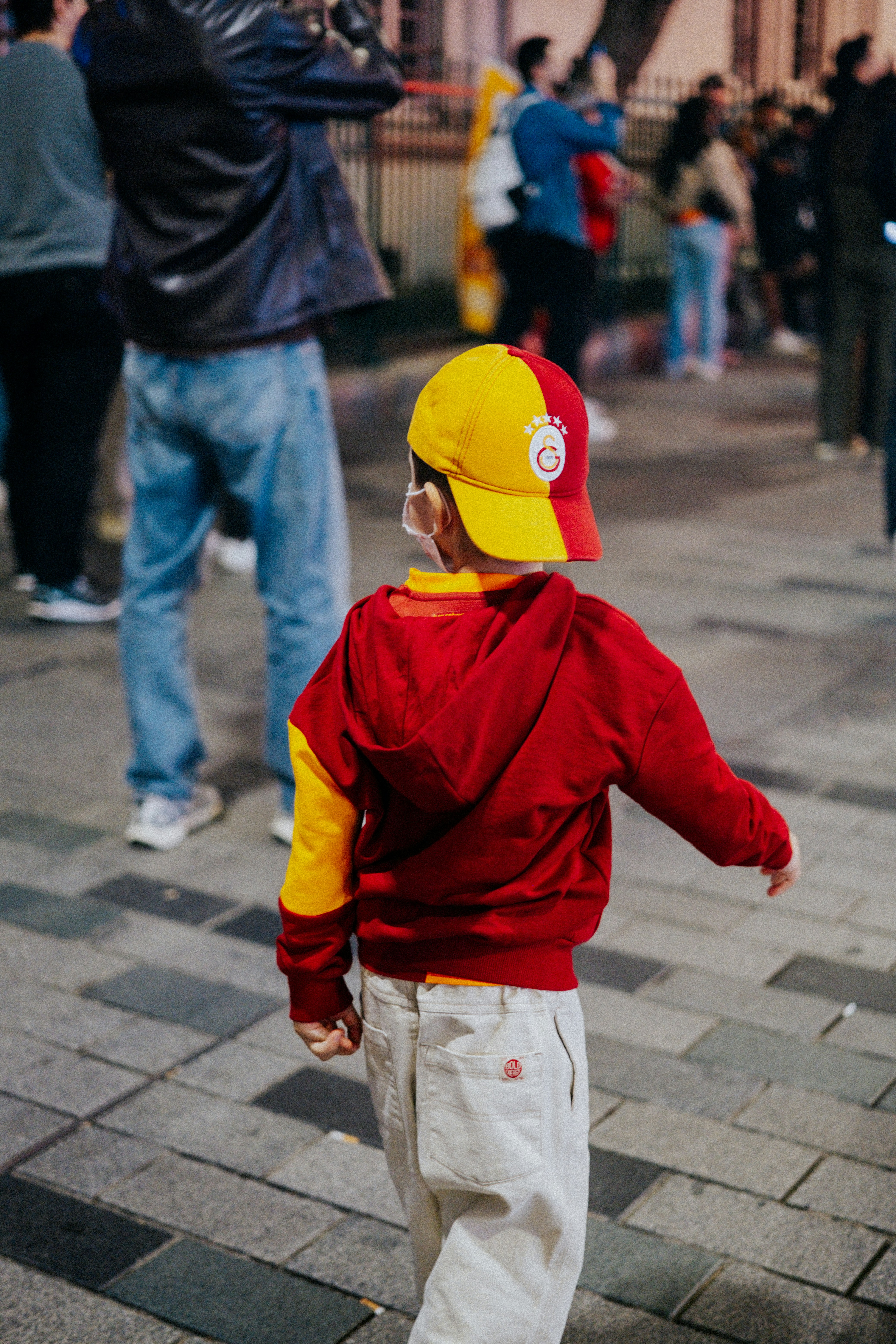 Colorful Child in Red Hoodie Faces Away in a Busy City Square