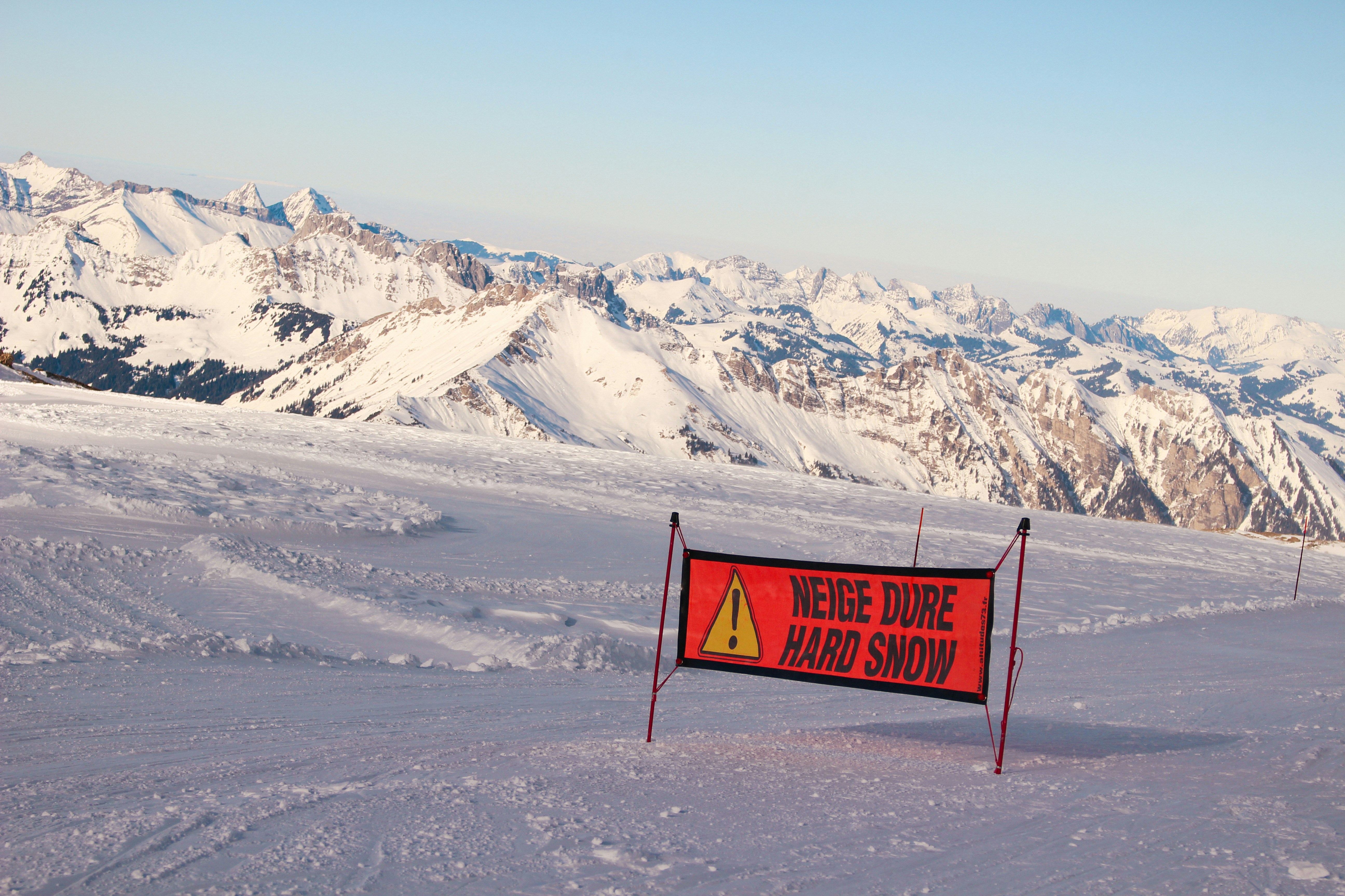 Warning at the White Ridge: Snowfield with Hazard Sign Against Alpine Backbone