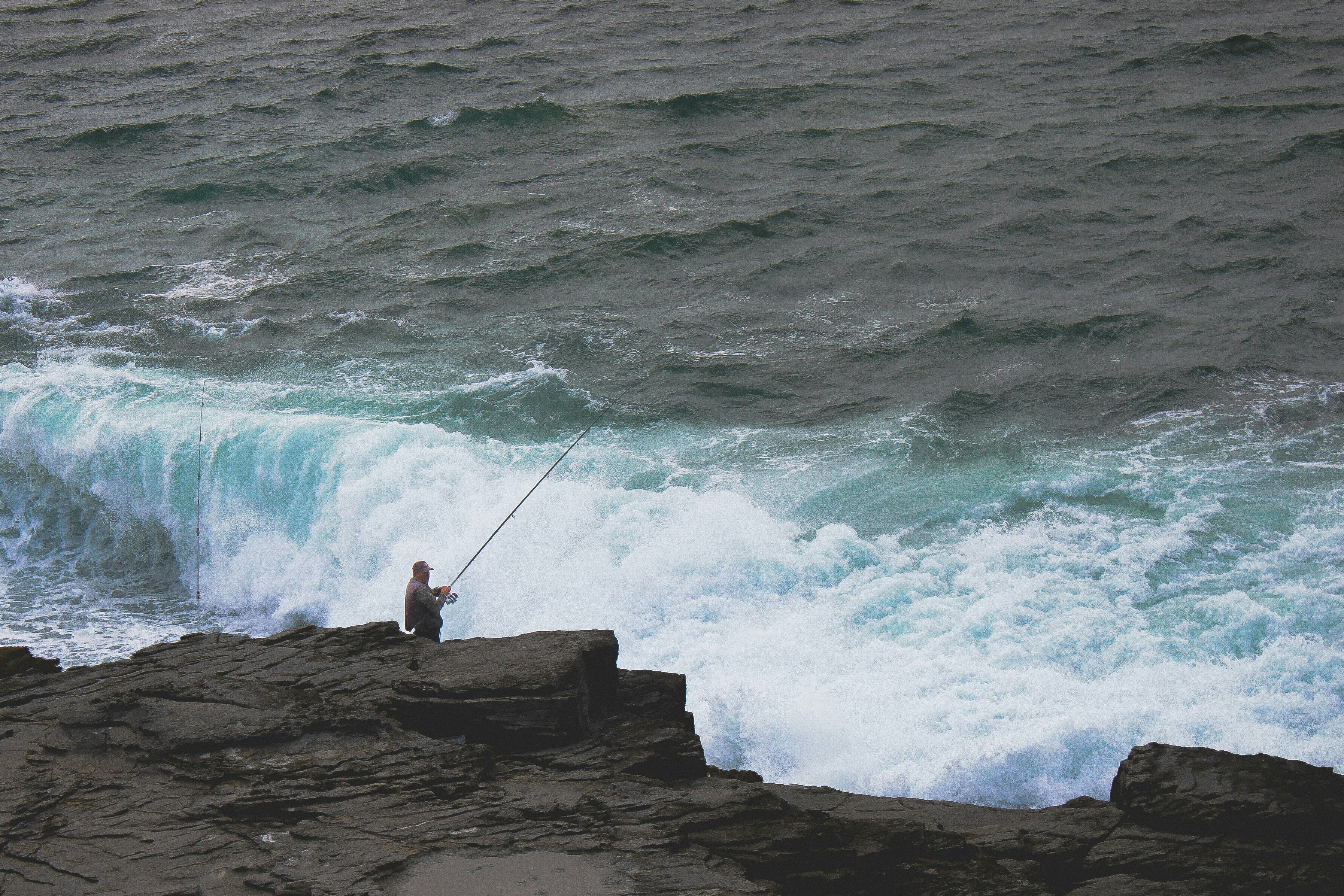 A person fishing from a rocky shore with large waves.