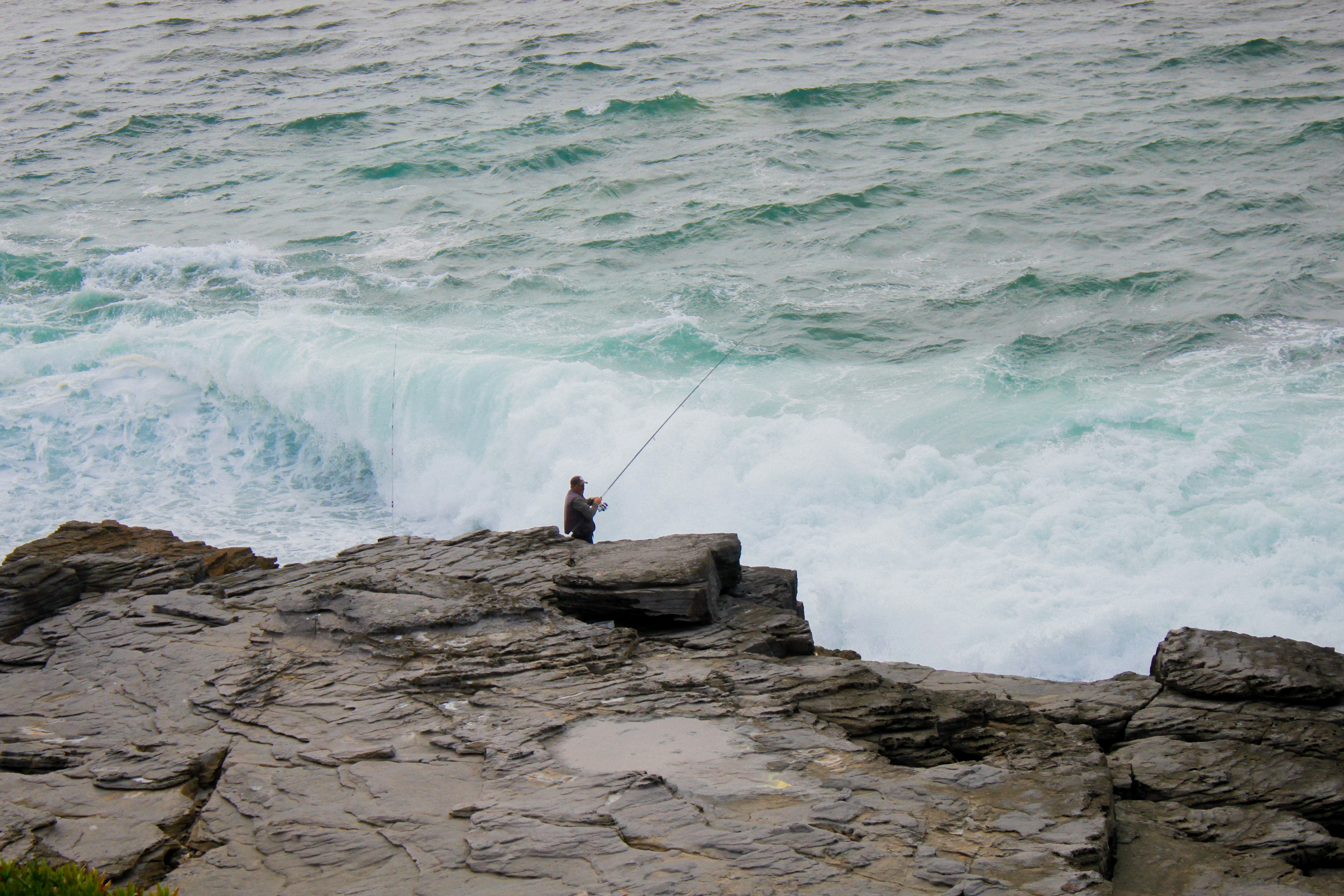  lone angler perched on basalt ledge against a surf‑driven horizon