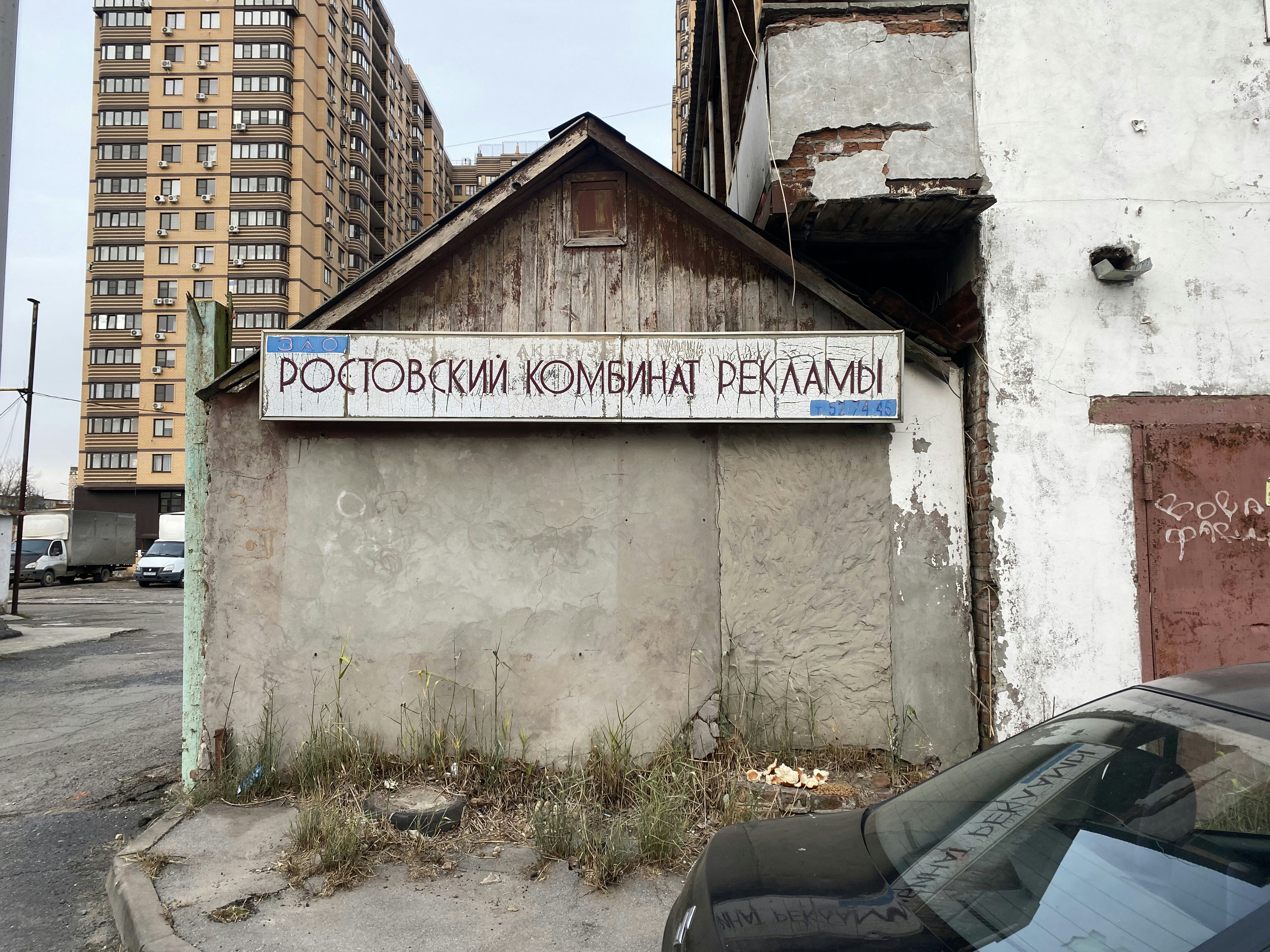Weathered storefront banner over a neglected lot with a backdrop of urban towers