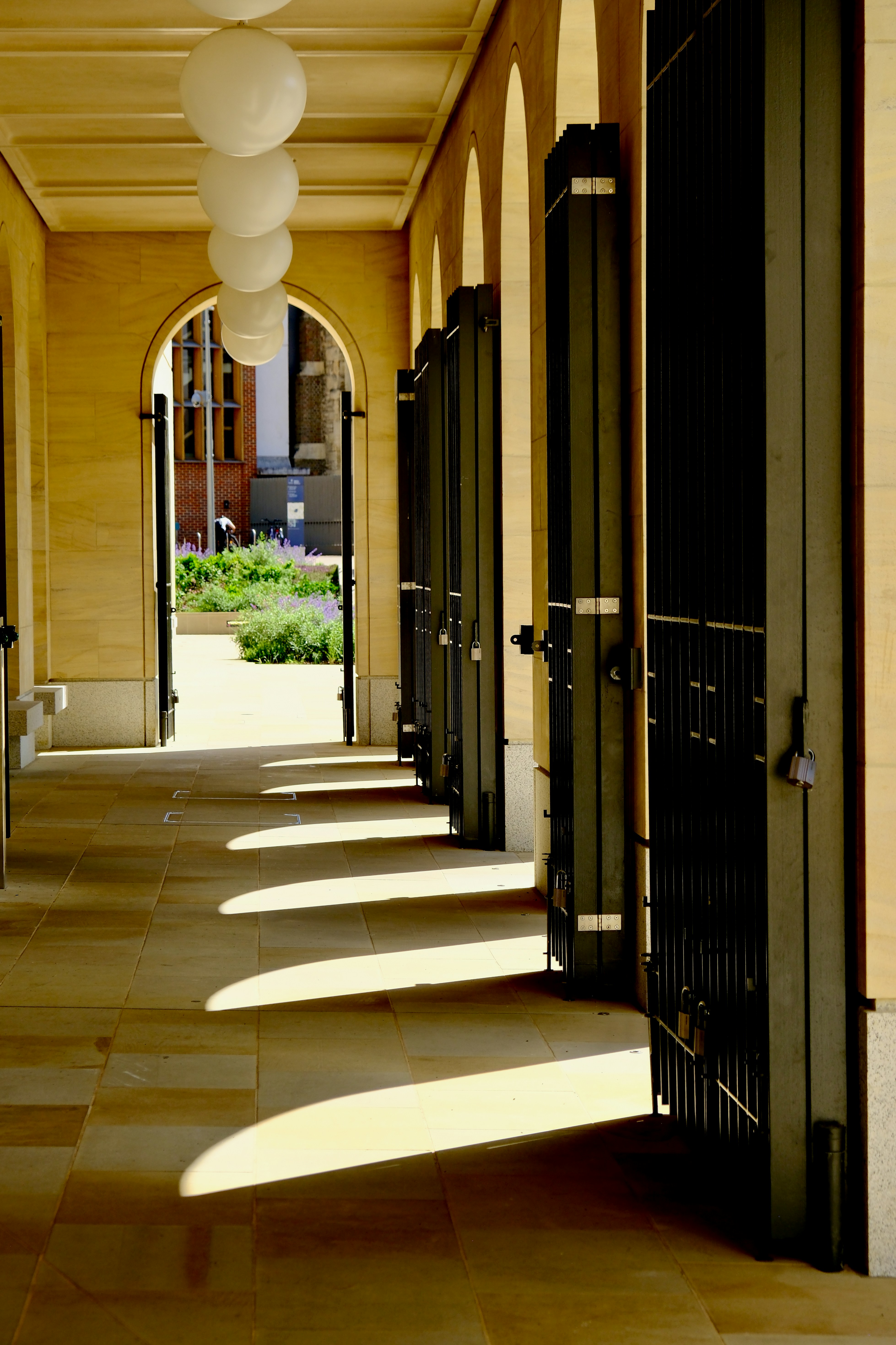 Arched stone corridor with open gates and dramatic sunlit shadows.