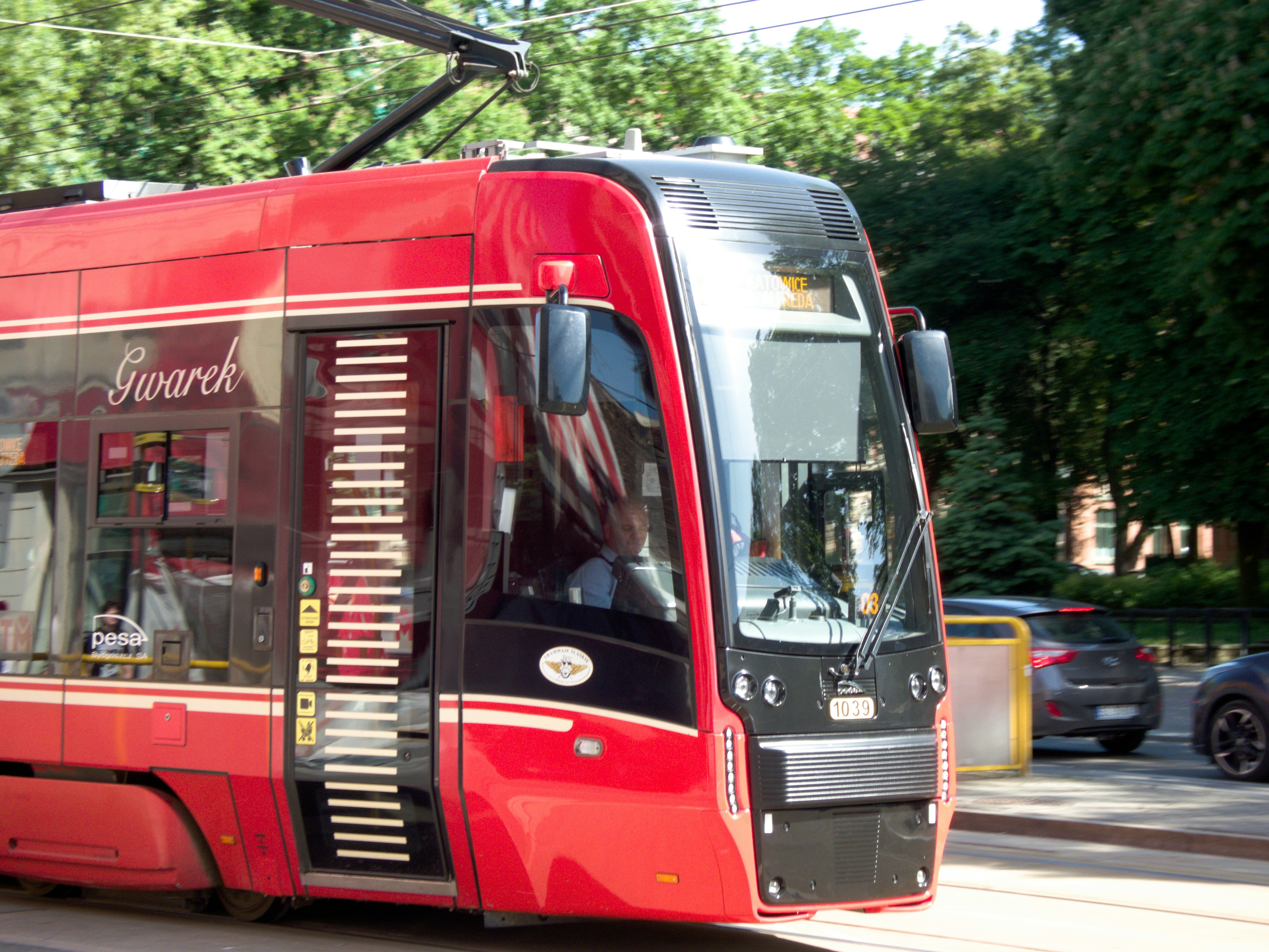 Red tram gliding past a tree-lined street