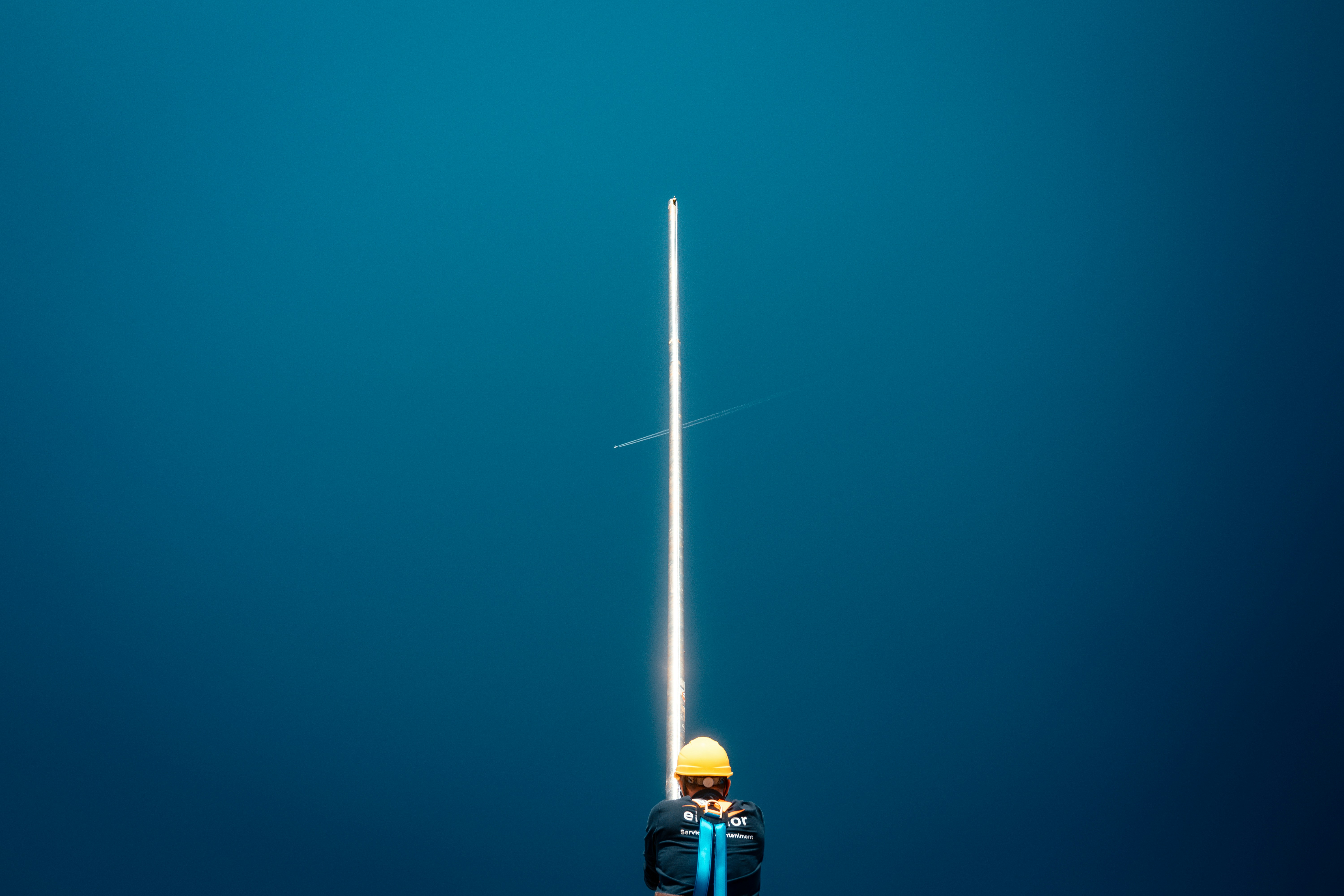 Vertical Beacon: A Technician's Silhouette Amid a Stratospheric Pole