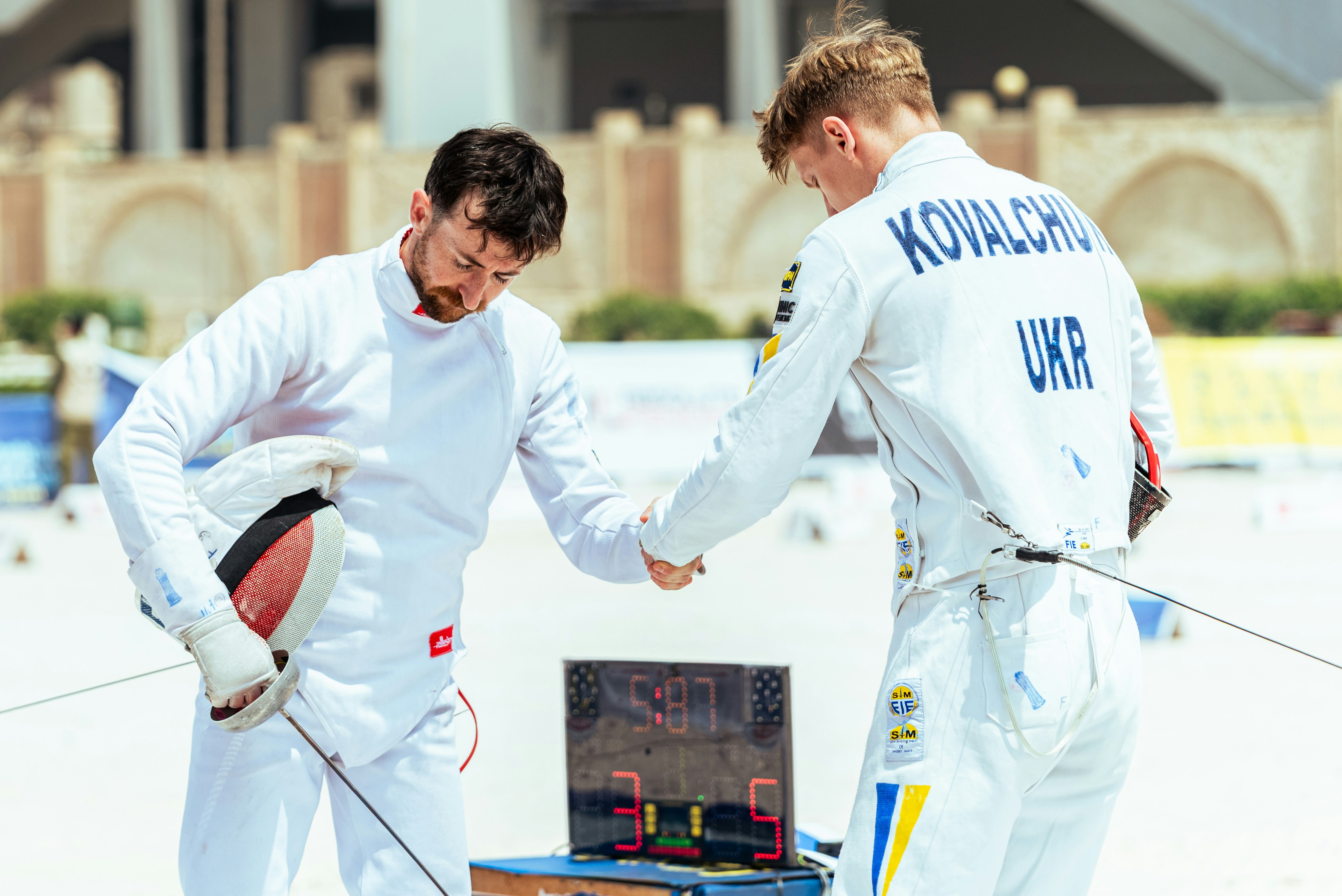 Two male fencers fist-bump after a competitive match.
