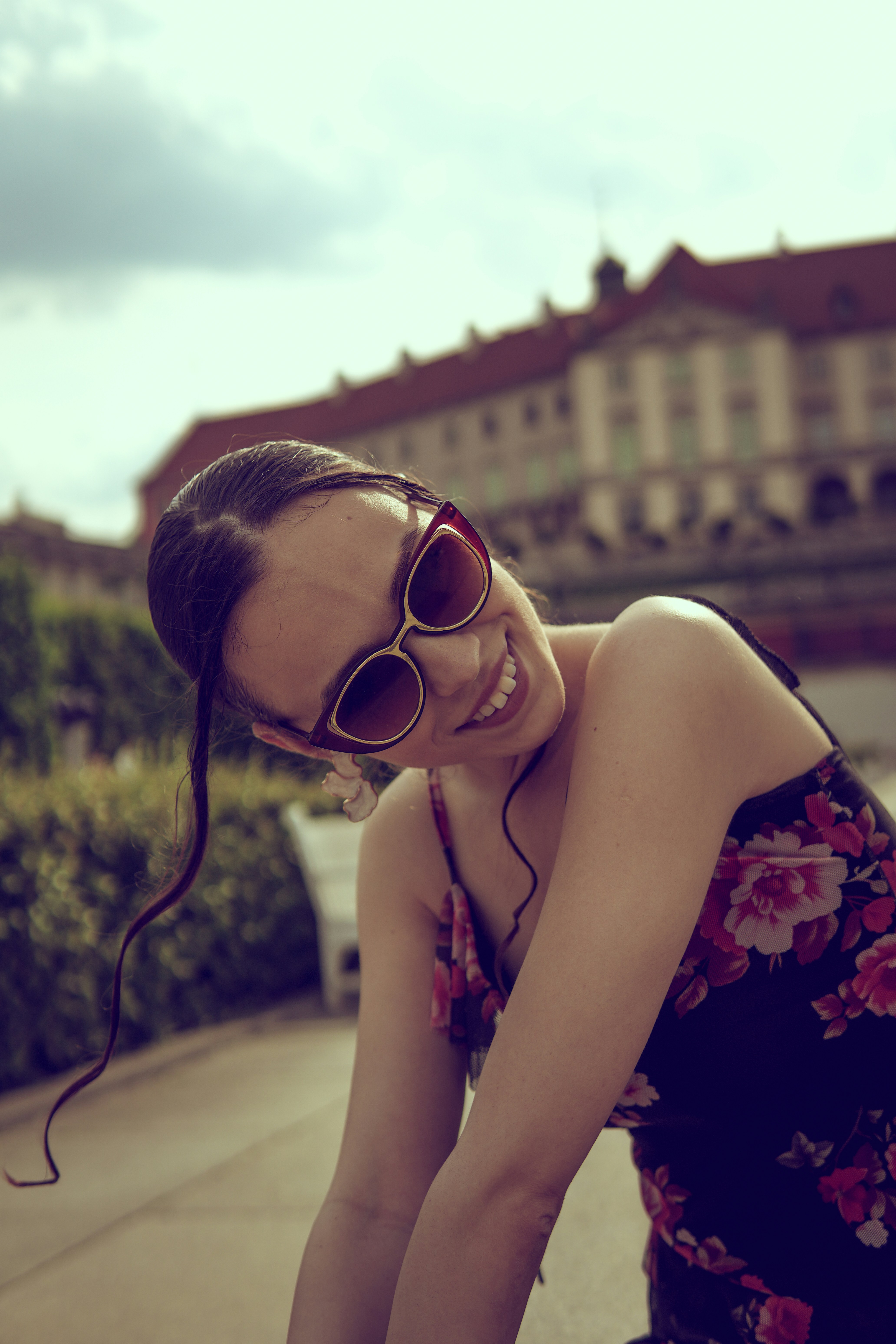 Stylish woman in floral dress and sunglasses smiling outdoors.