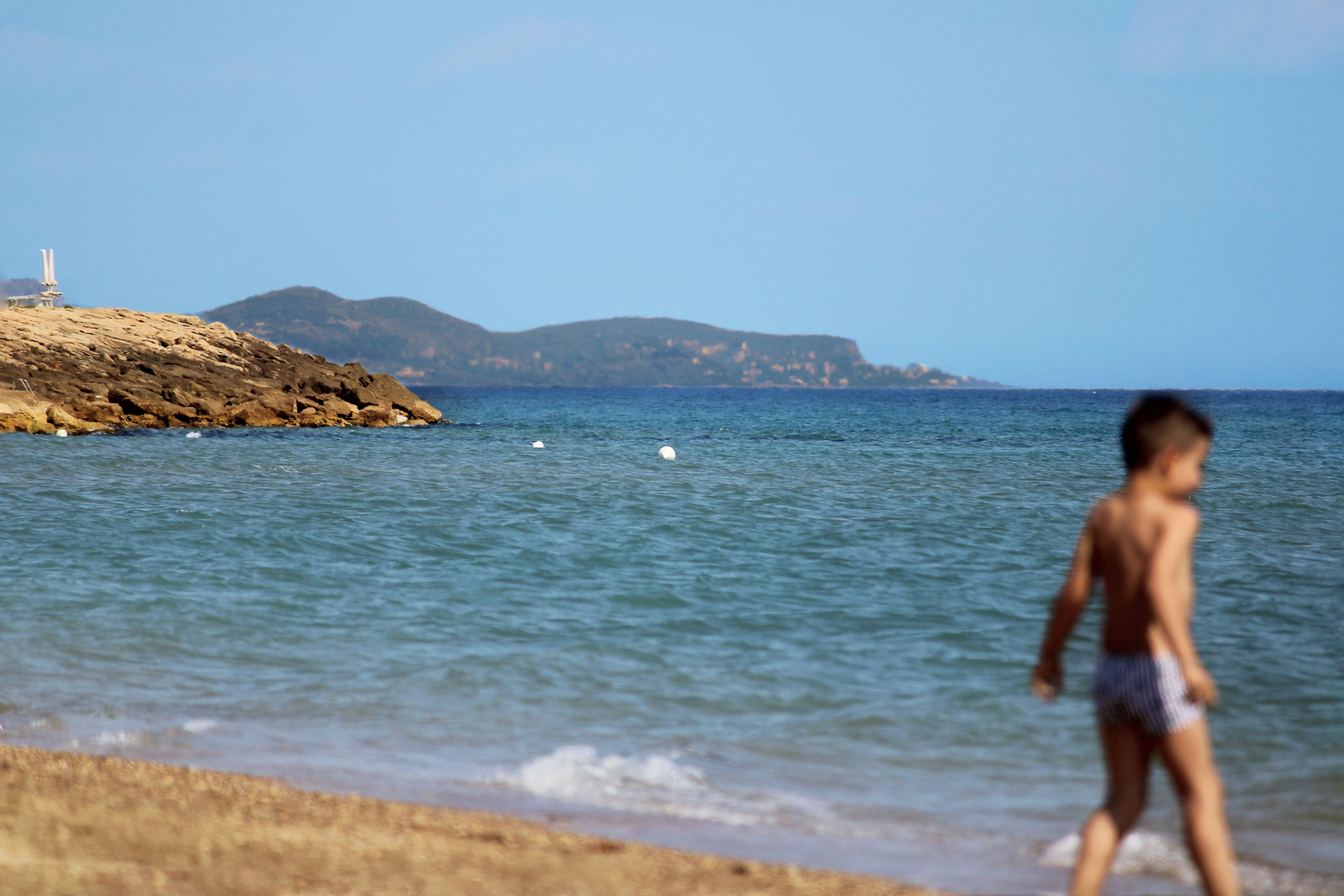 Sunlit shoreline with distant headland and a solitary jogger