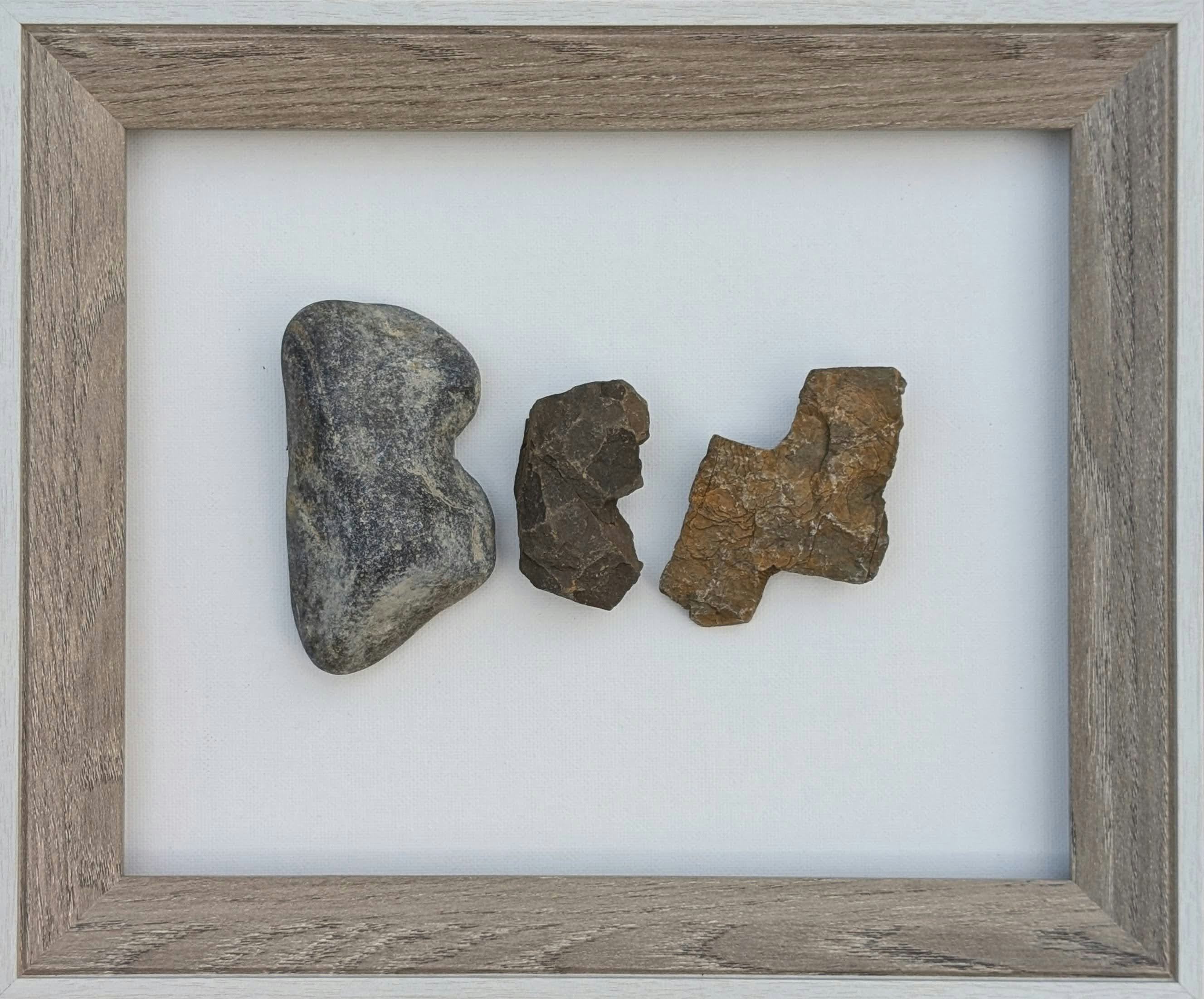 Three Pebble Fragments on White Canvas Within a Framed Still Life