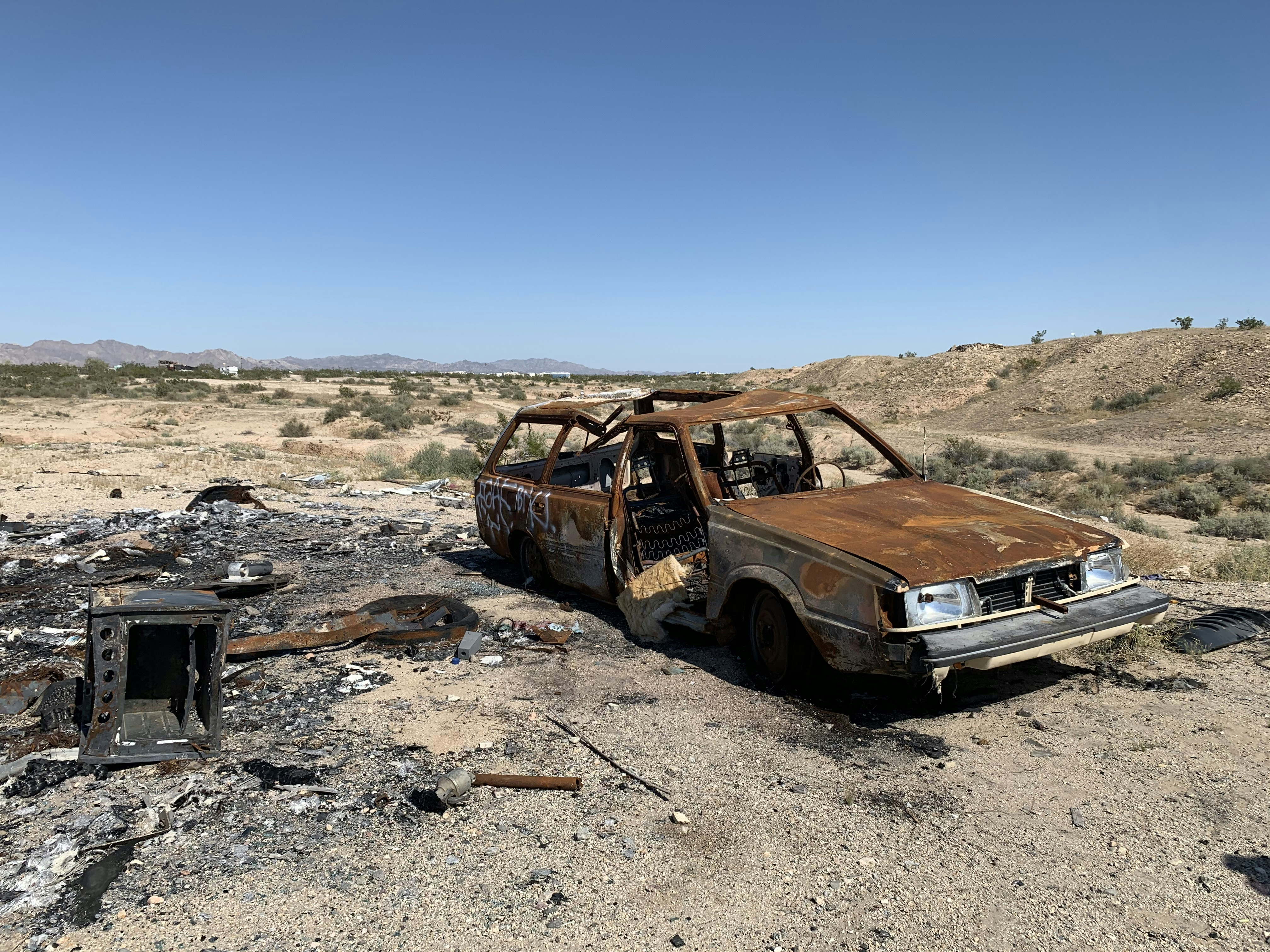 Charred Relic in a Desert Wake: A Rusted Car Among Ash and Scatter