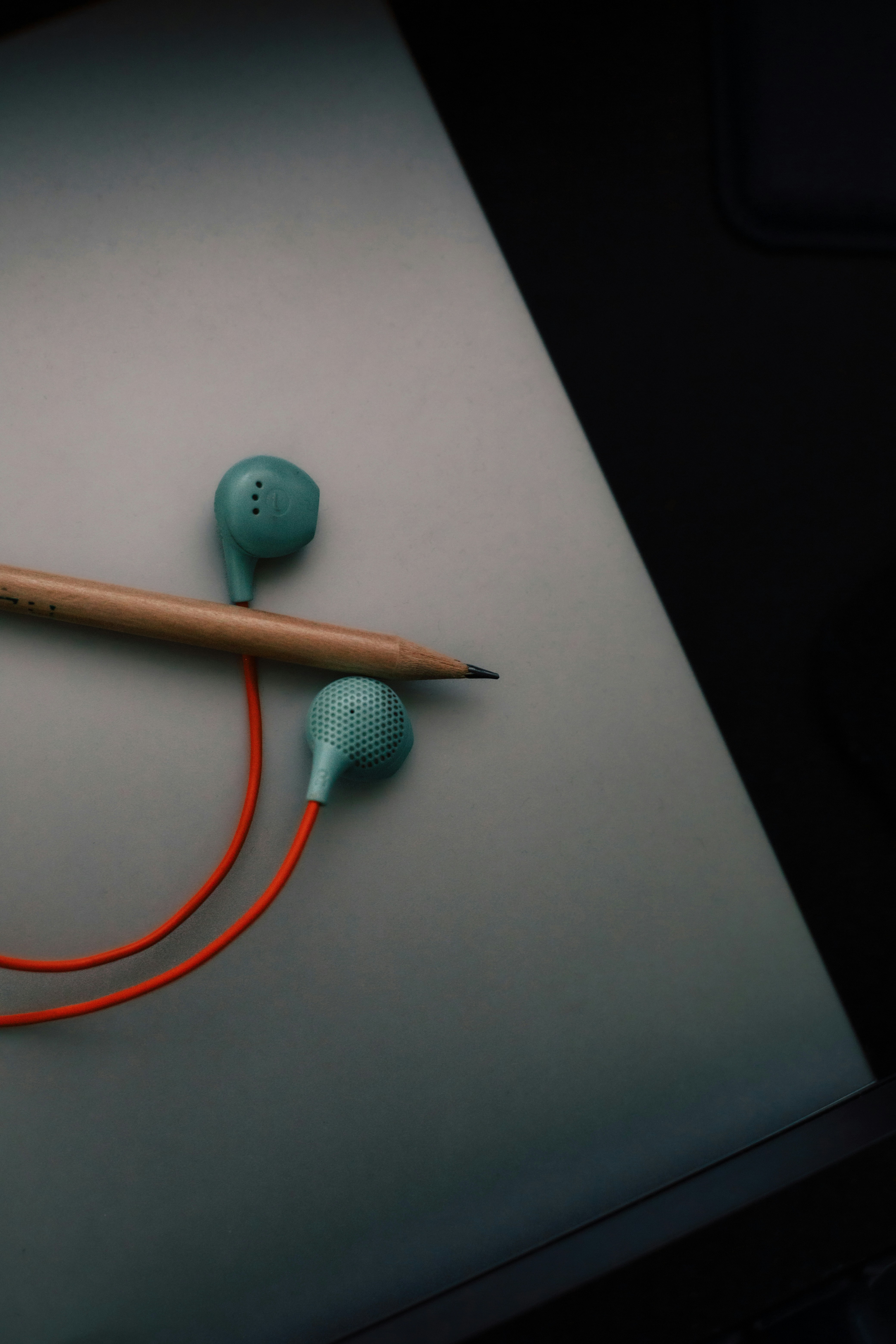 Teal Earbuds and Pencil Rest on a Slanted Desk Edge