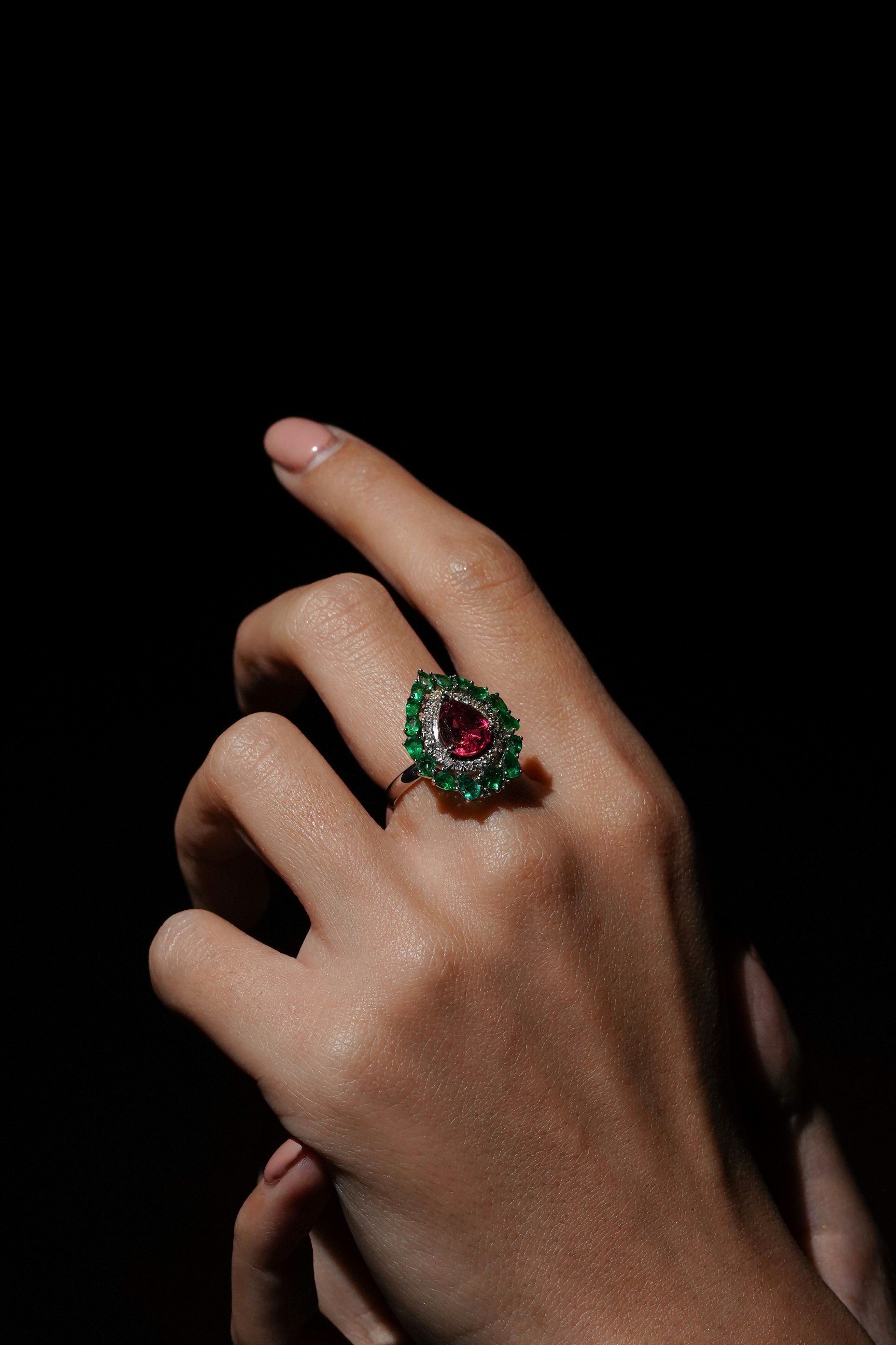 Emerald Halo: A Hand Adorned by a Ruby-Centered Ring in Spotlight