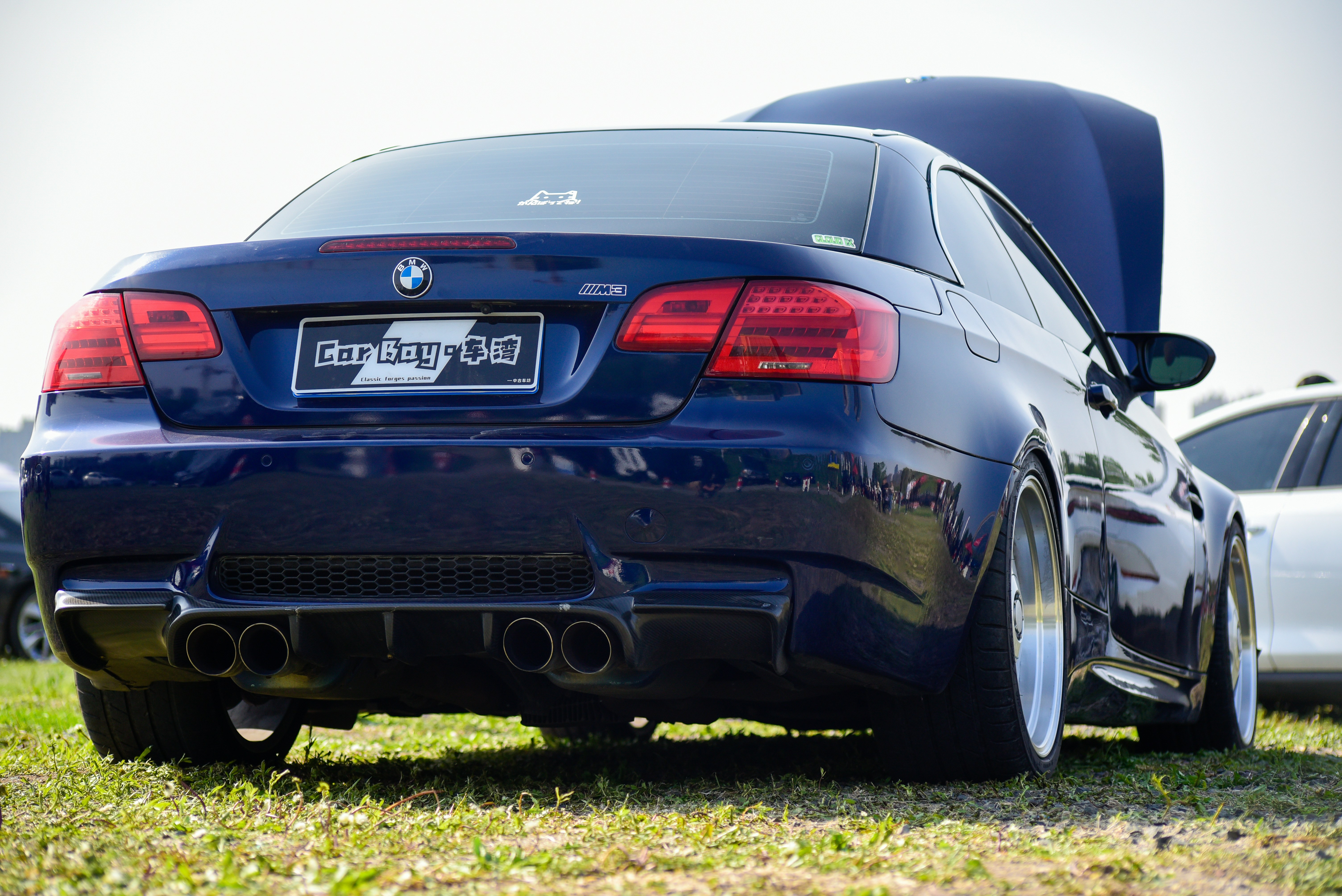 Low-slung BMW silhouette: rear quarter with open hood reveal at a car show