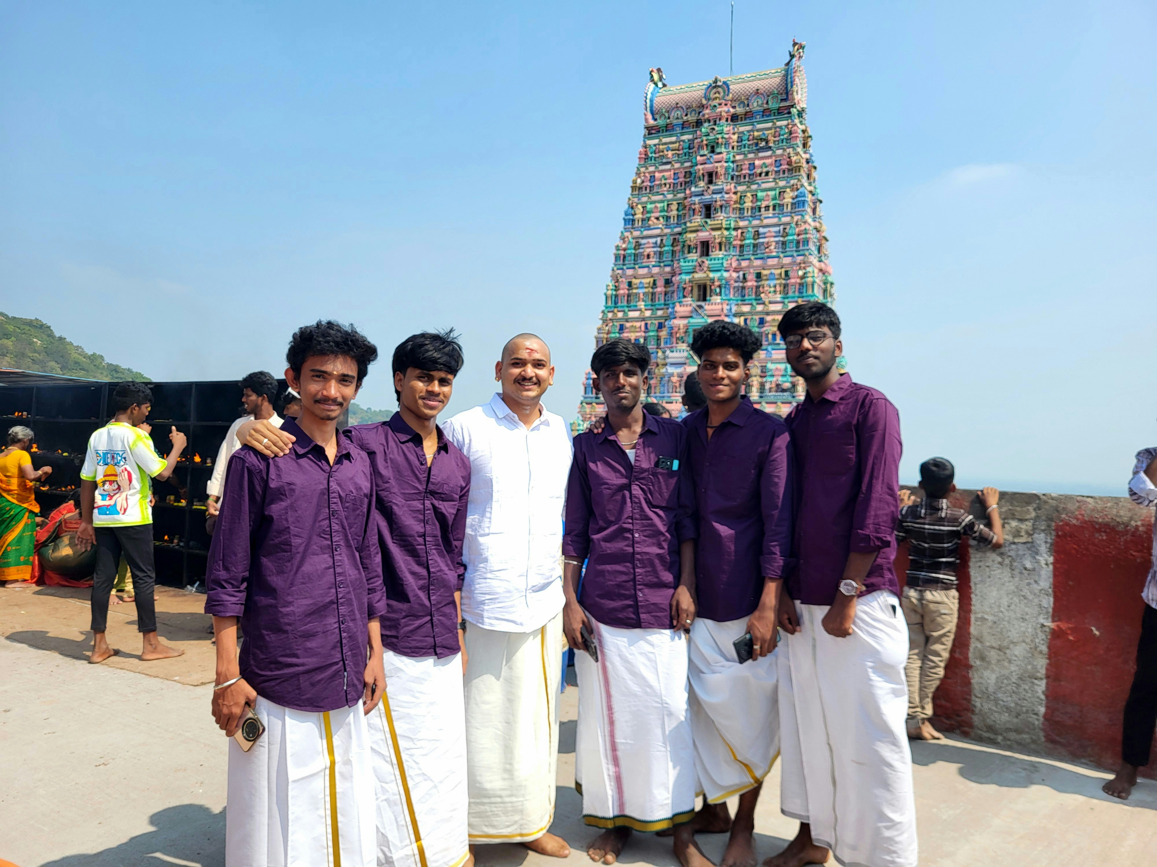 Group of men in traditional attire posing before a temple gopuram