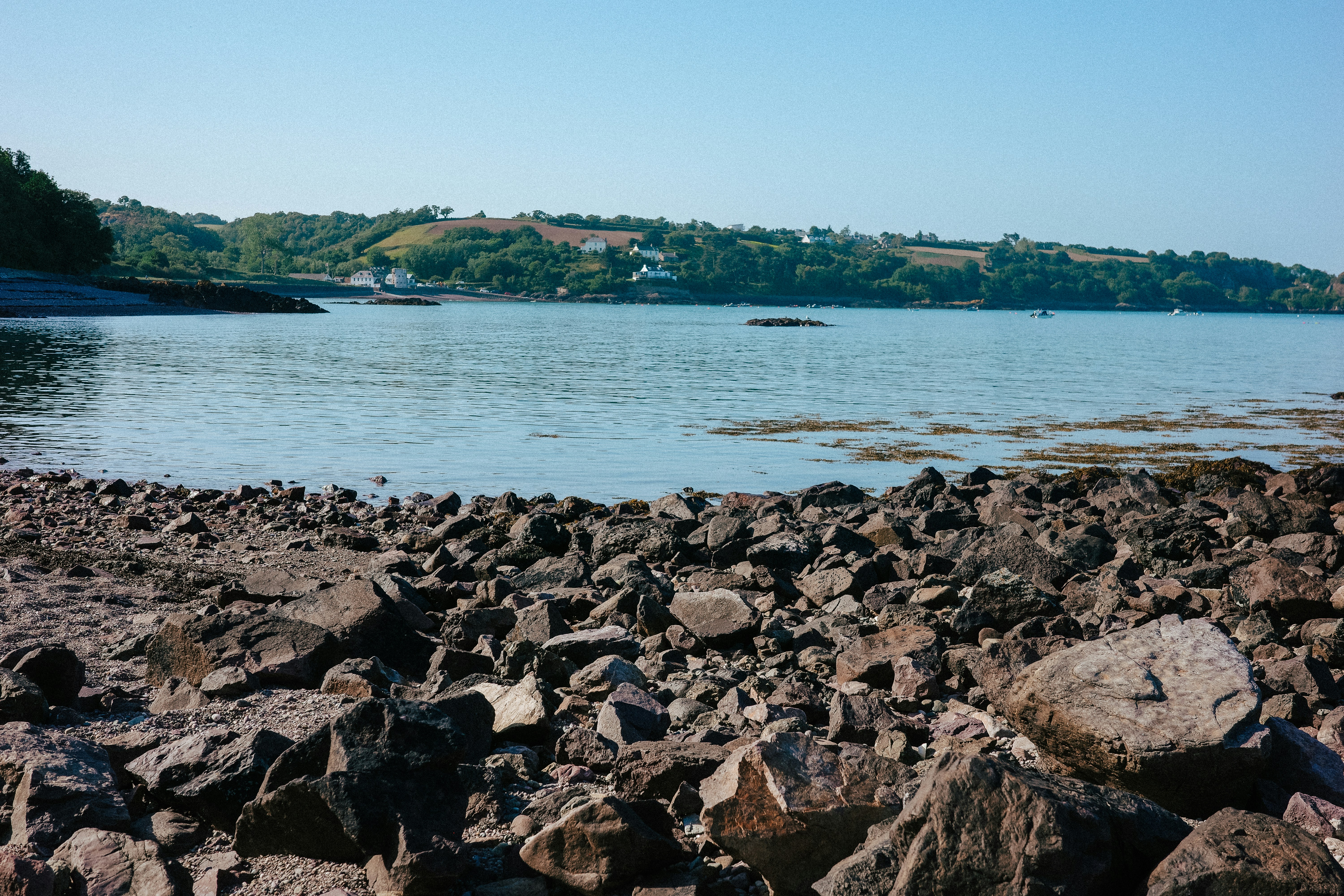 Calm bay with a rocky foreground and green hills.