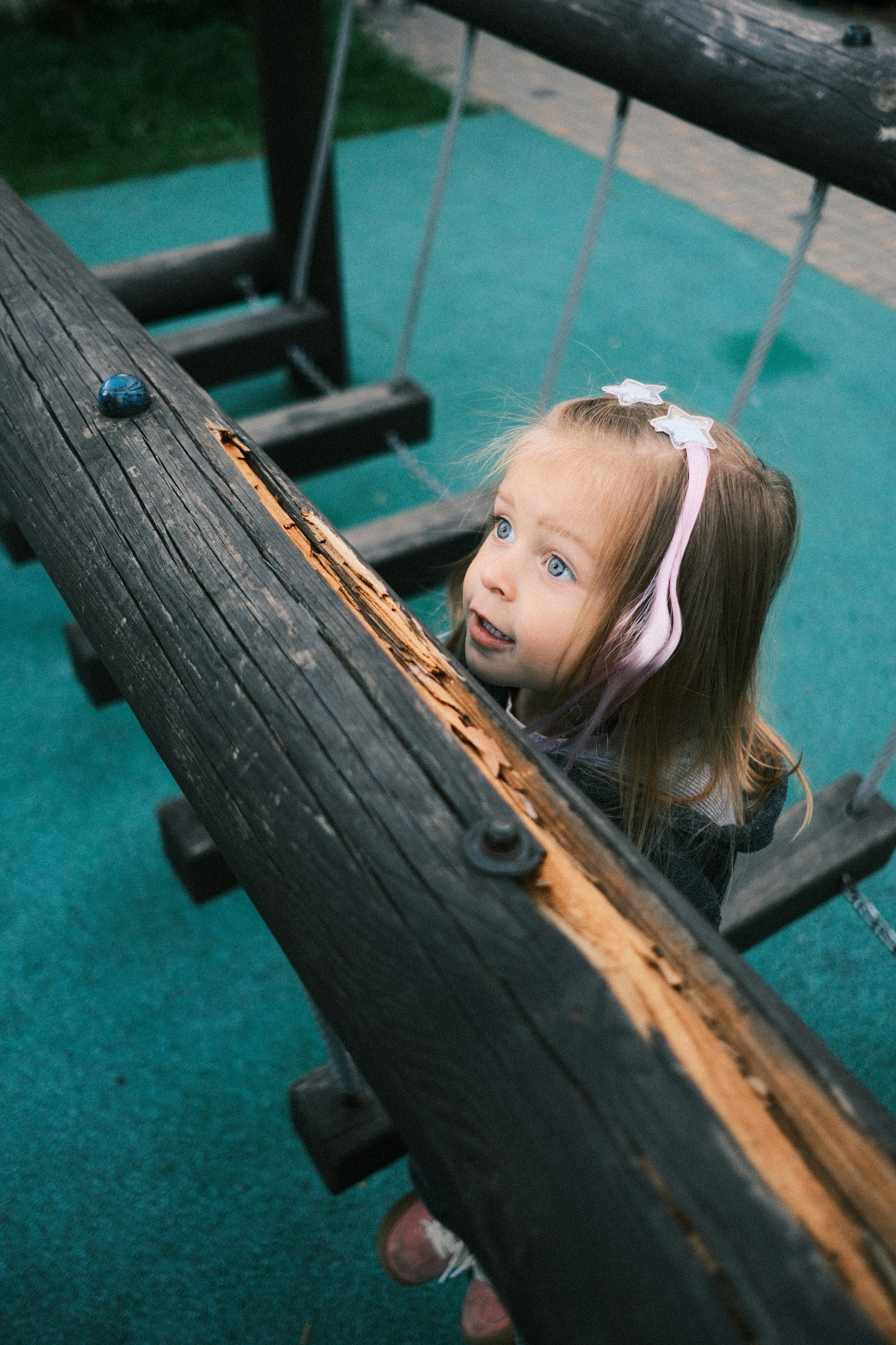 A young girl playing on a wooden playground structure.