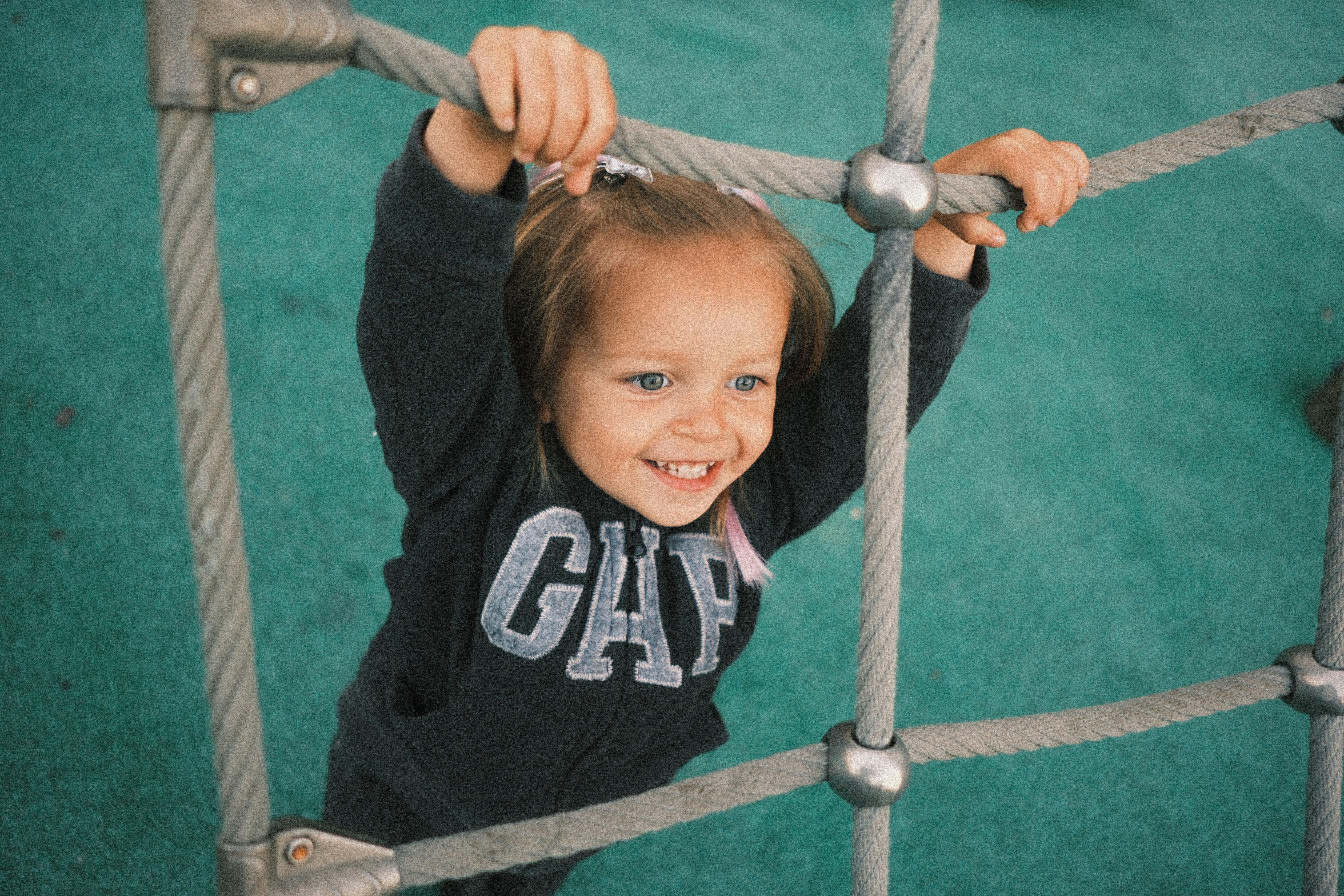 Grinning explorer grips a rope net in a sunlit playground