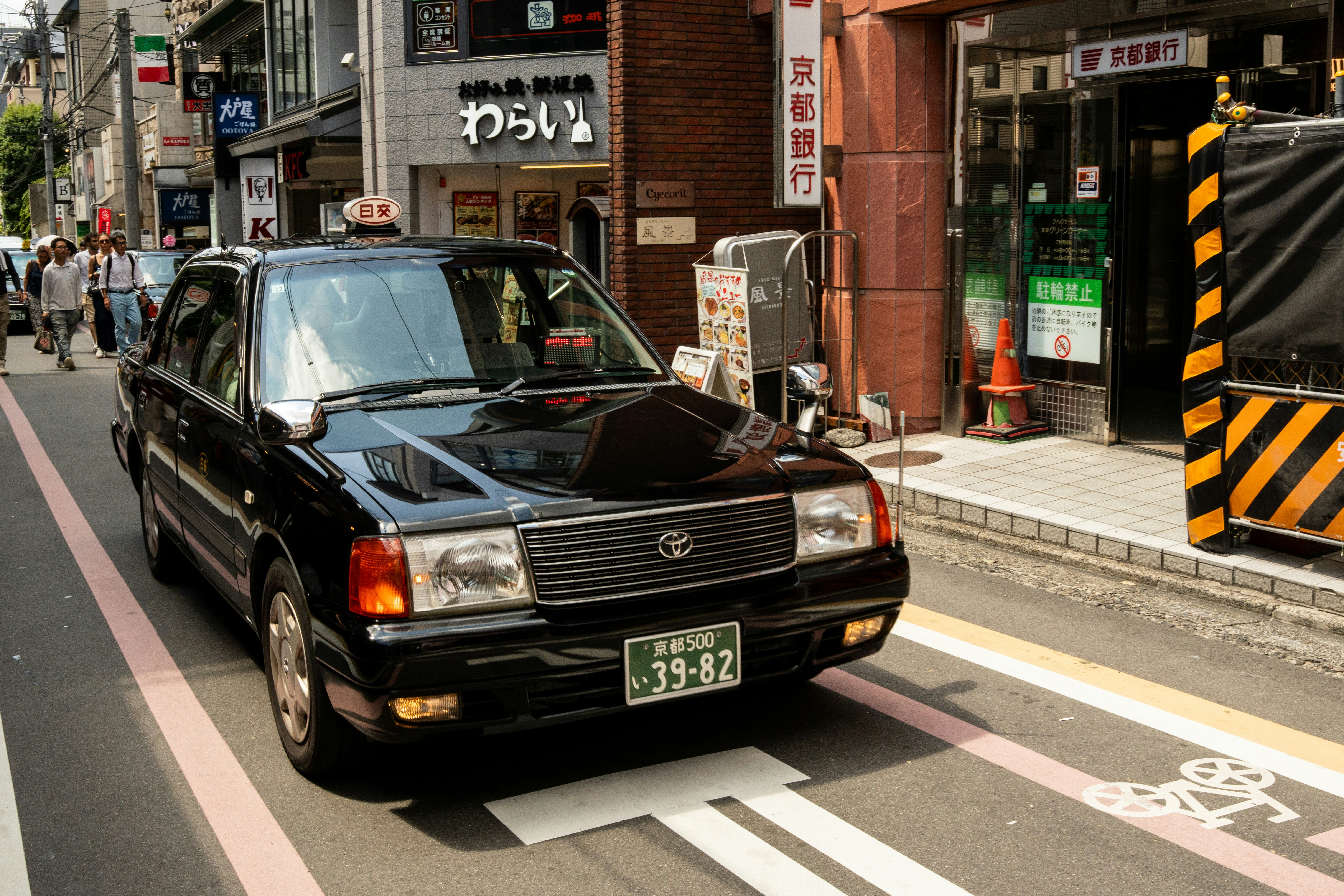 Black taxi on a busy Tokyo street with signs and storefronts
