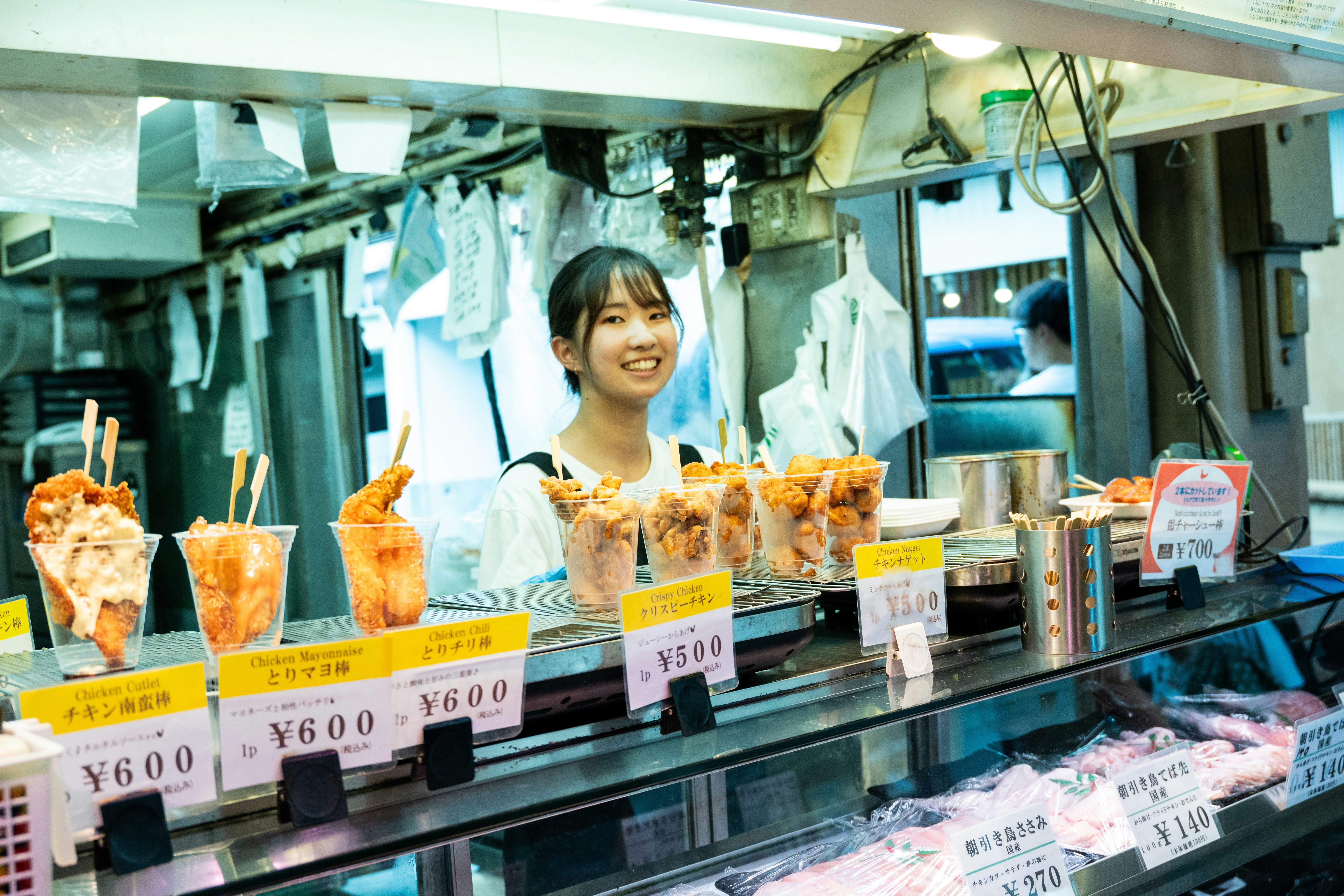 Smiling fry vendor behind a glass counter brimming with skewered katsu-style treats
