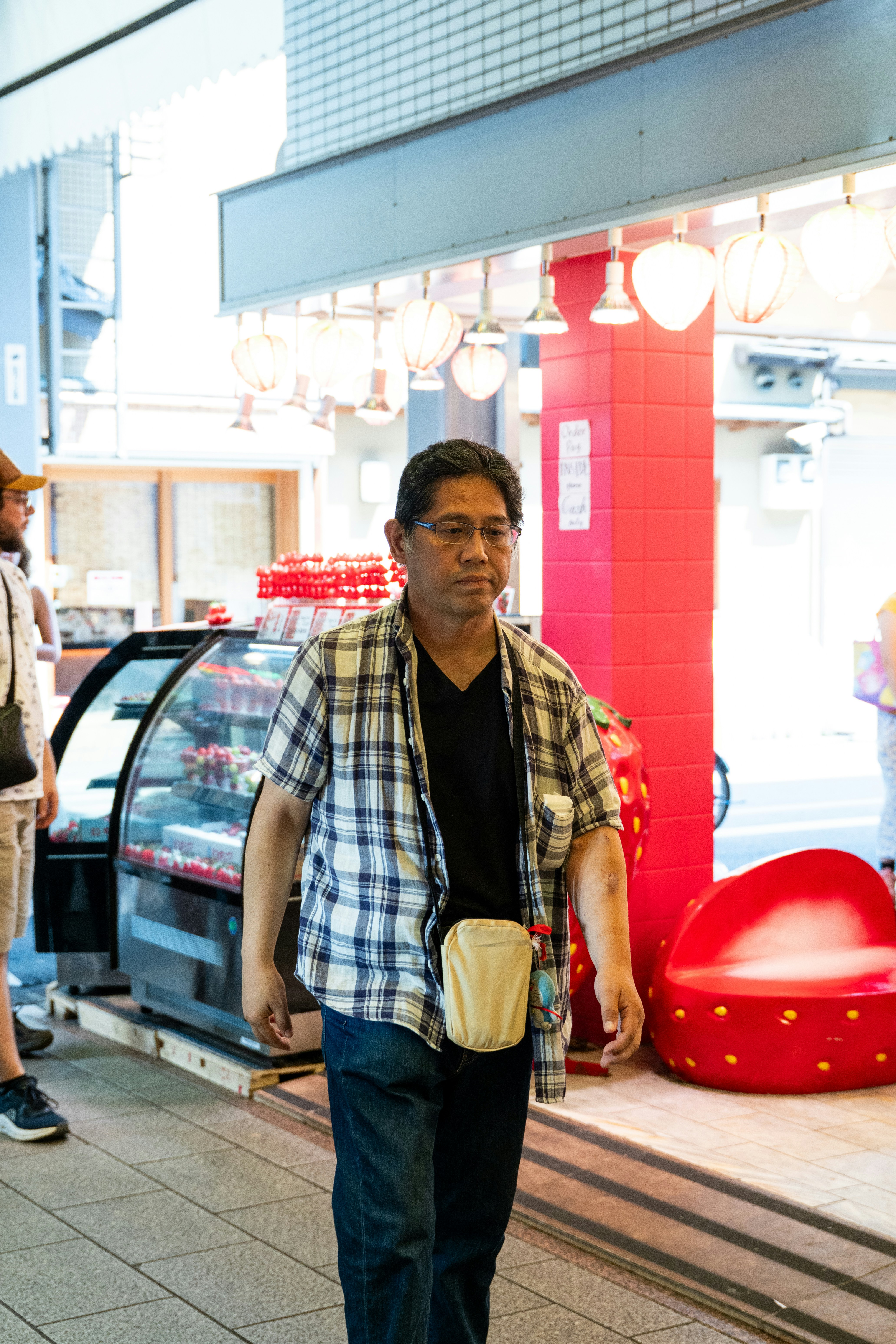 Man in checkered shirt walking past a storefront with red decor and display case